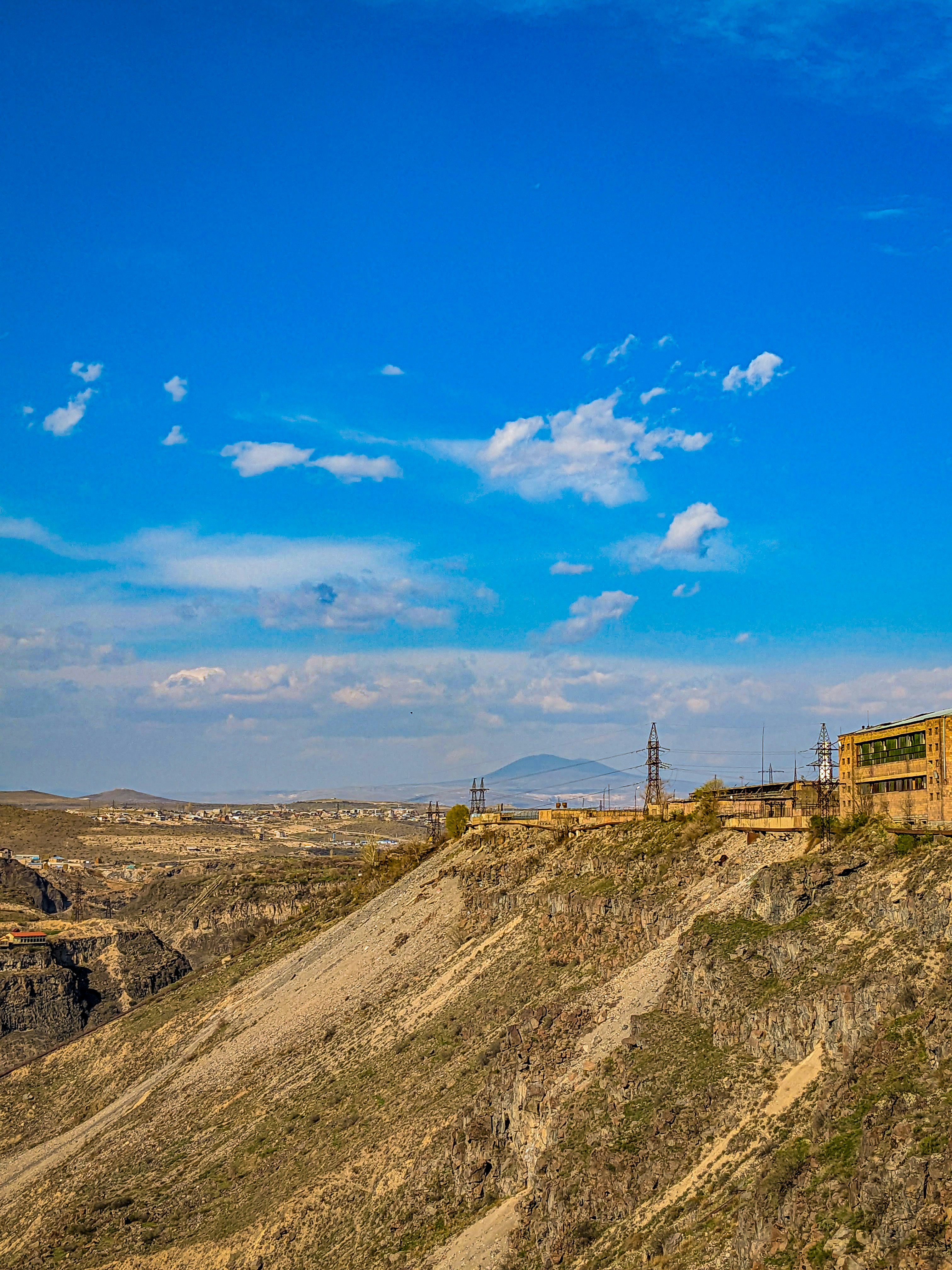 Rugged quarry lip with institutional buildings and utility pylons along the ridge under a bright sky.