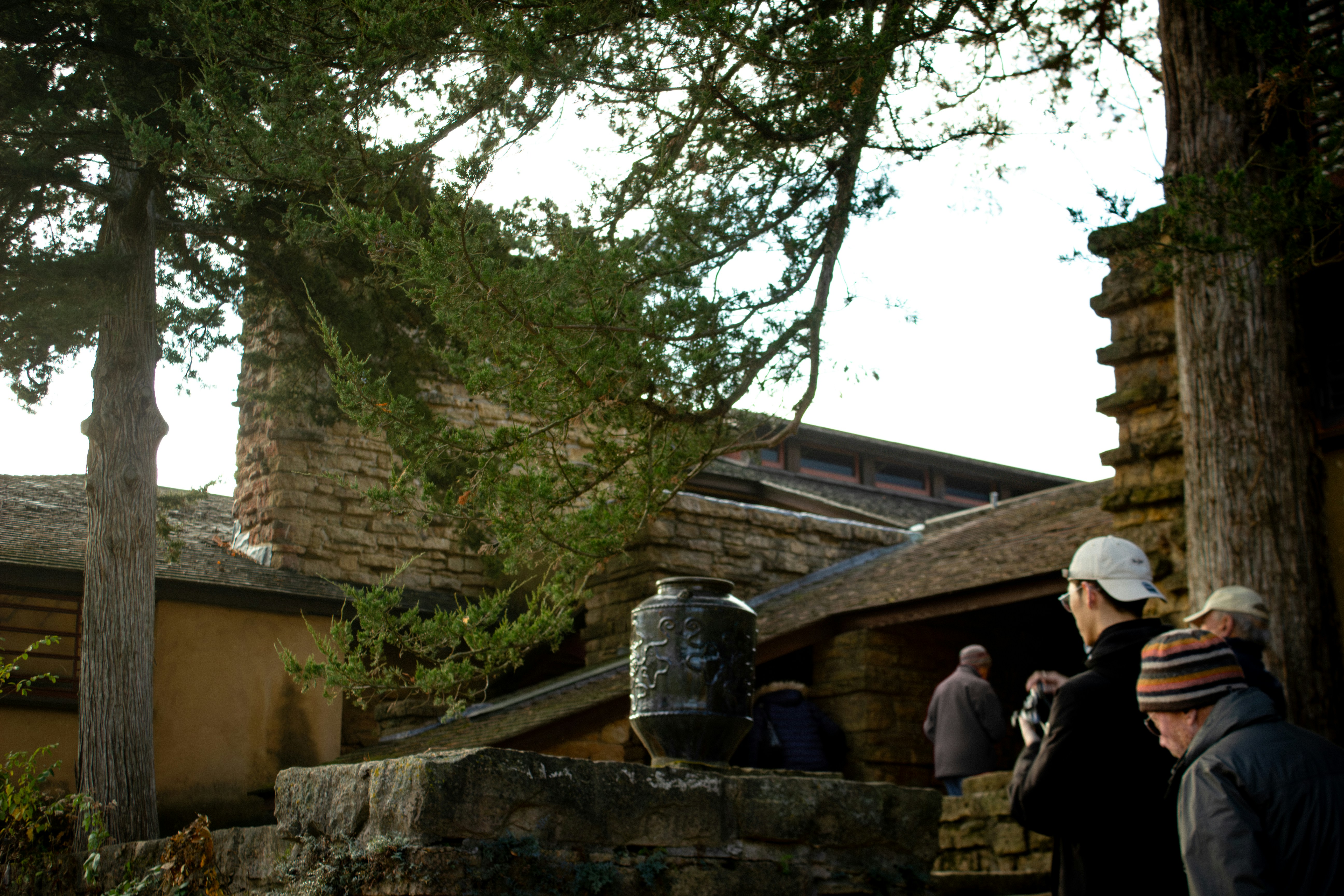 Quiet Courtyard Moment: A Weathered Jar among Visitors Beneath Stone Architecture