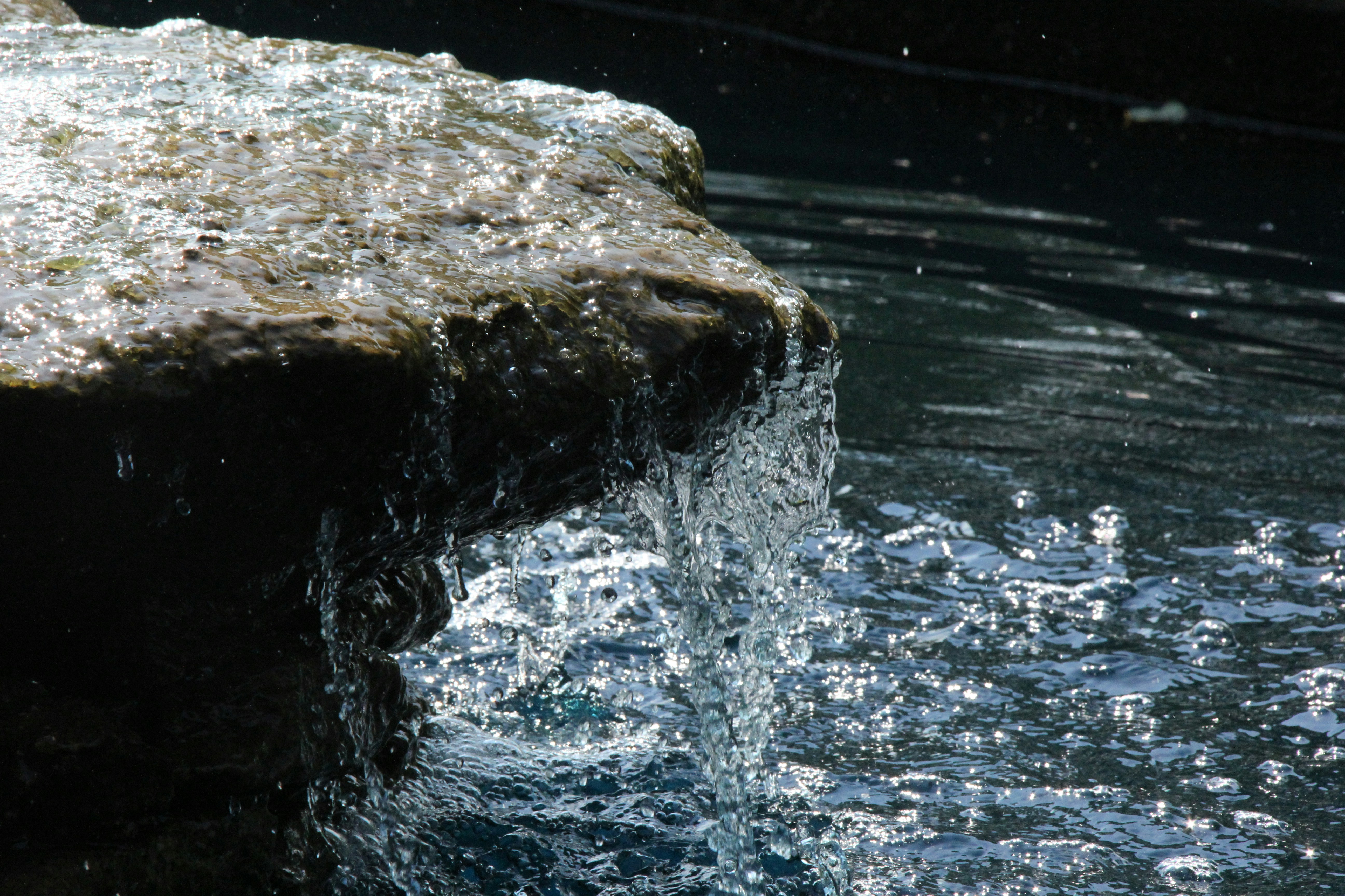 Water gently cascading over a rock into a dark, rippling pool.