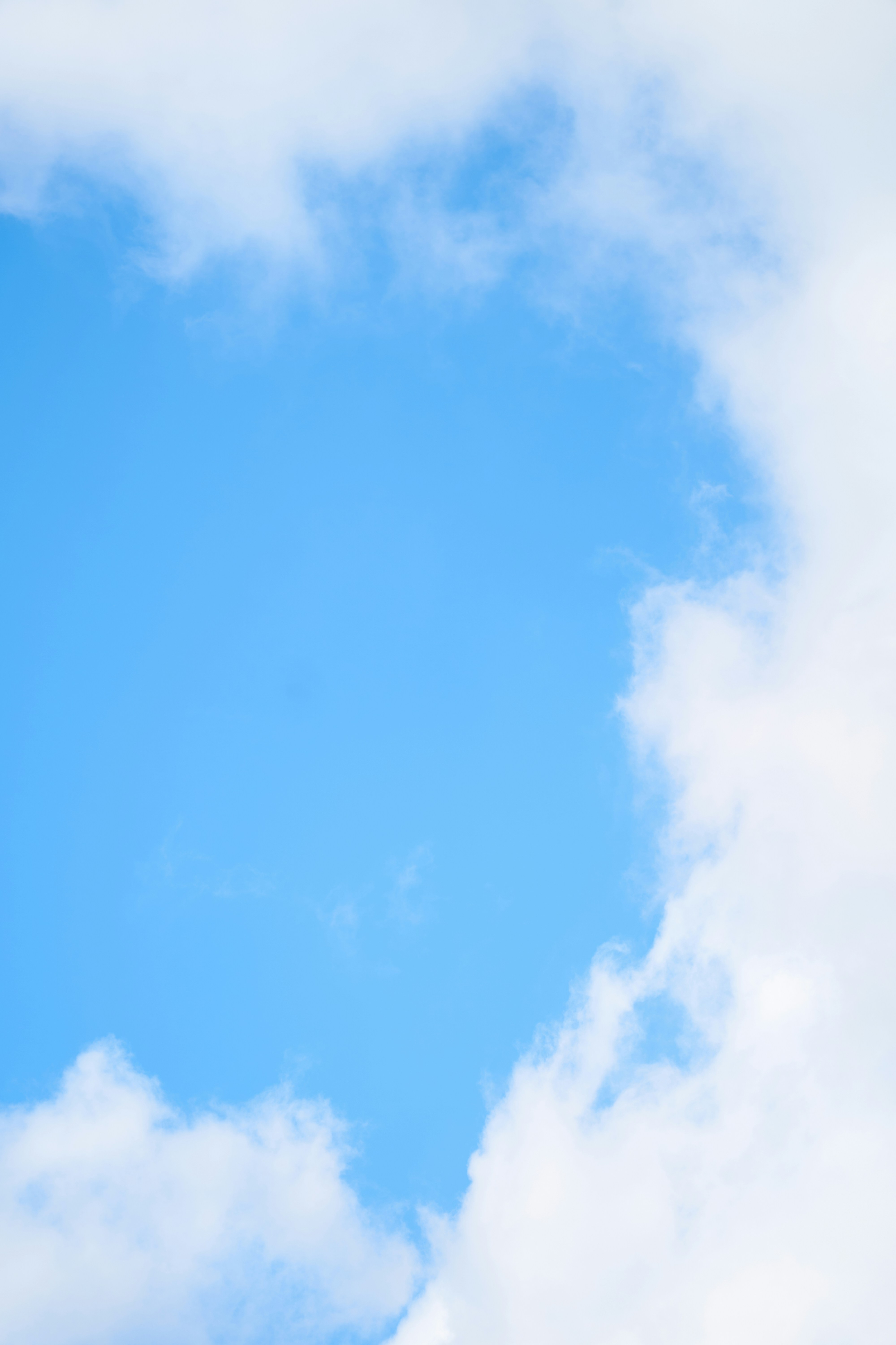 A vibrant blue sky framed by soft, fluffy clouds, creating a serene atmosphere. The composition highlights the contrast between the sky and the clouds.