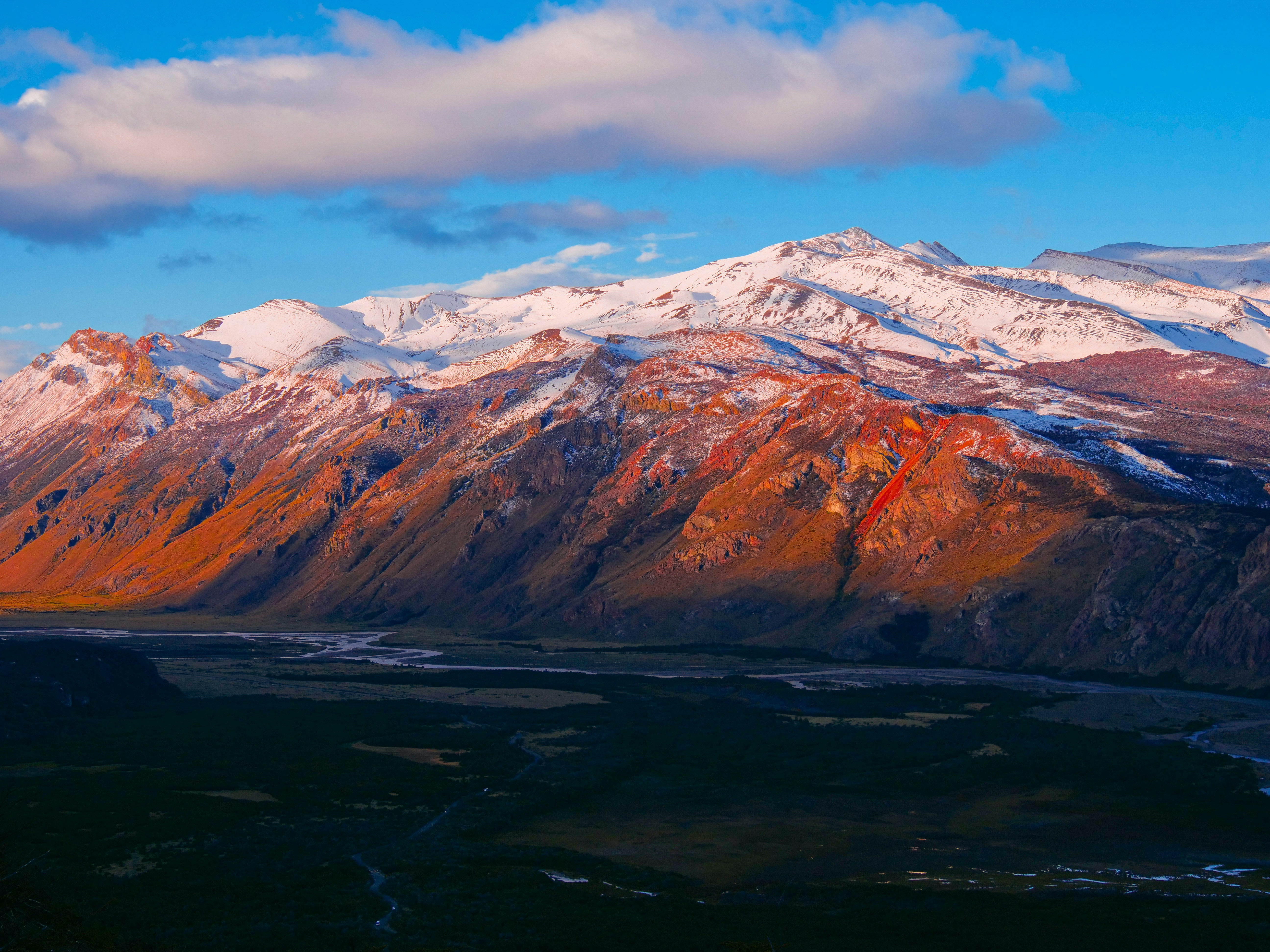 Snow-capped mountains bathed in warm sunrise hues under a vibrant blue sky.