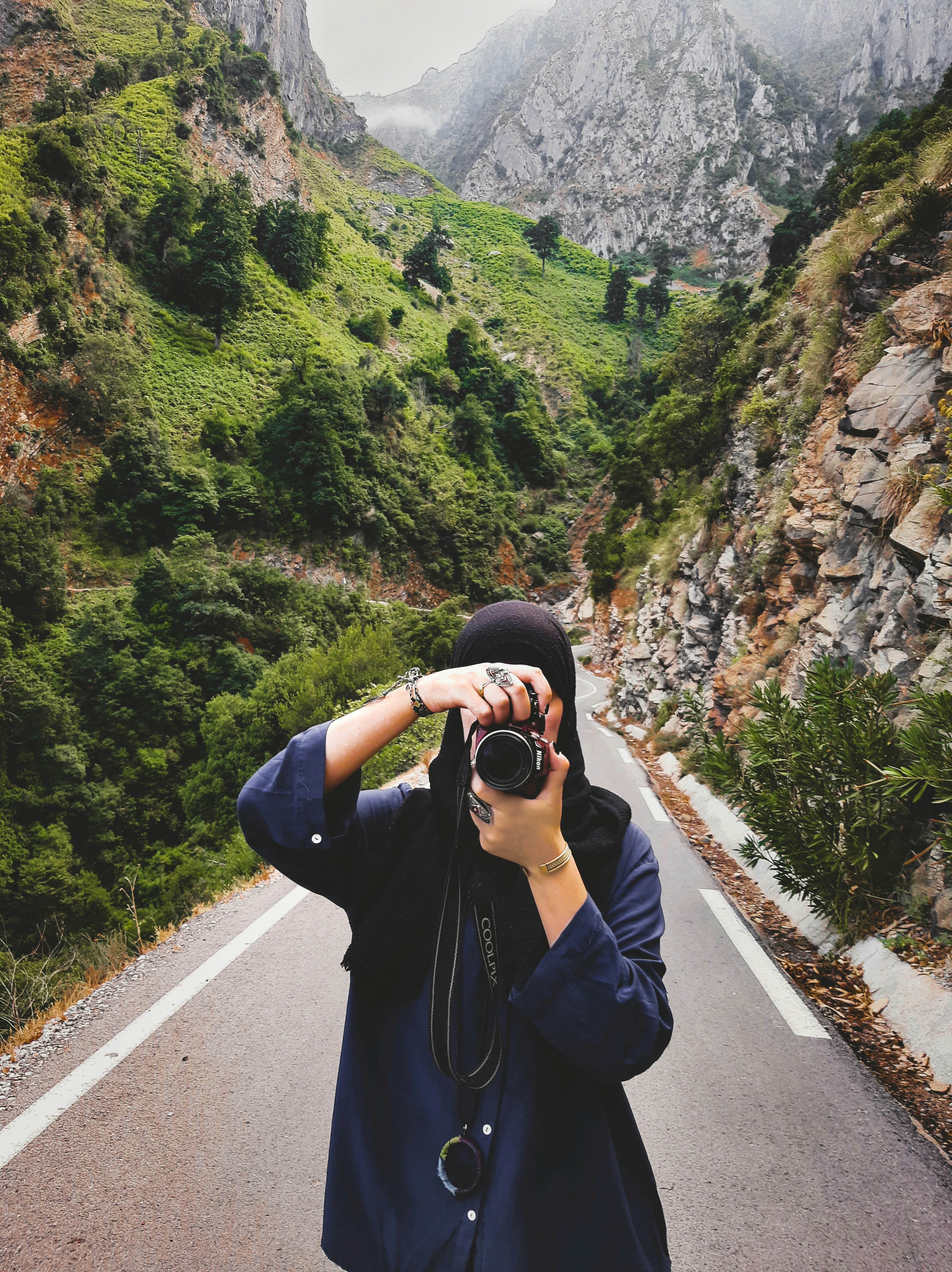 Portrait on the Mountain Pass: A photographer on a winding road among green cliffs