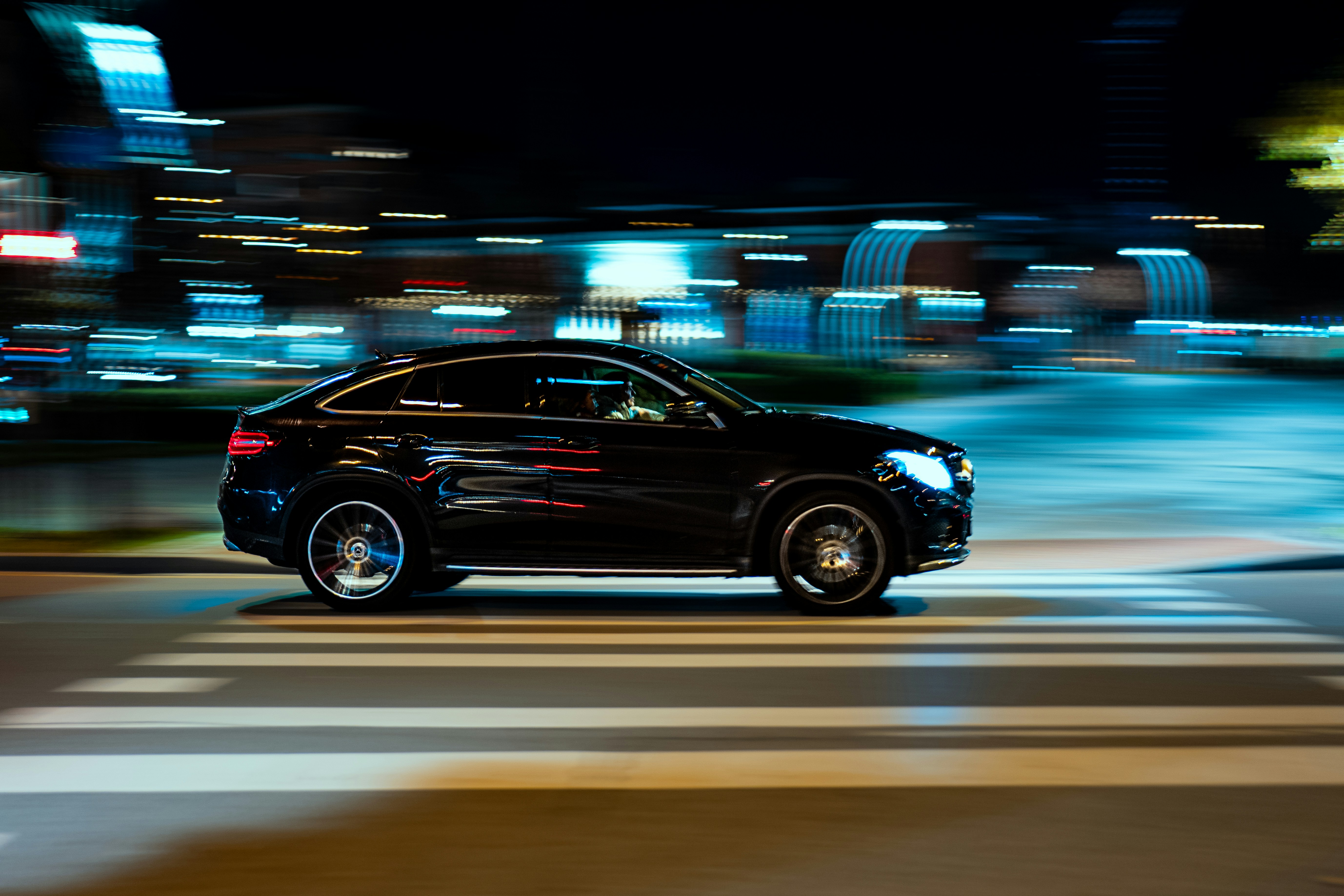 Black car speeding through a city street at night, with motion blur highlighting the urban lights.