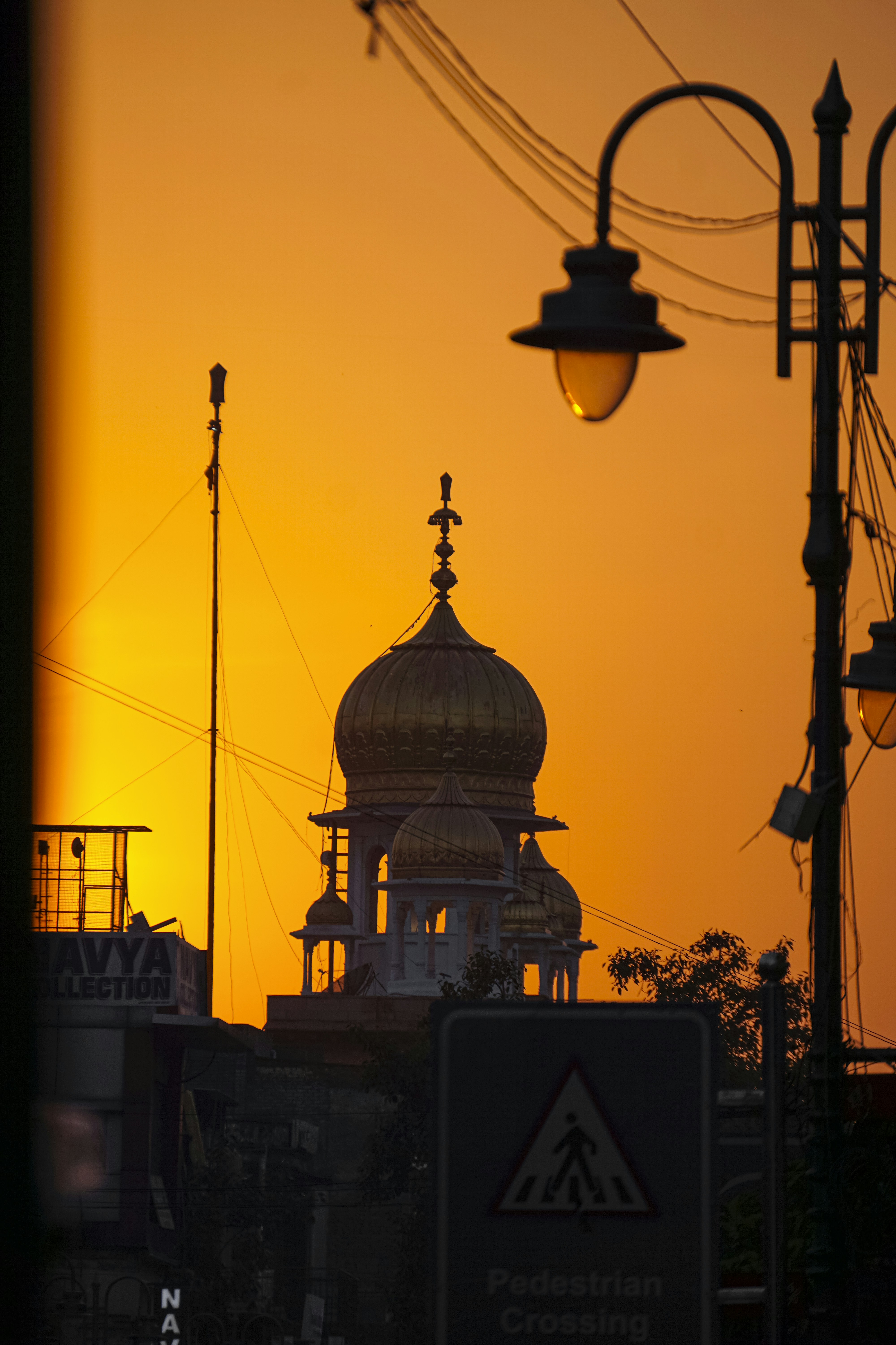 Silhouette of a domed structure framed by a vibrant orange sunset, with street lamps and urban elements in the foreground.