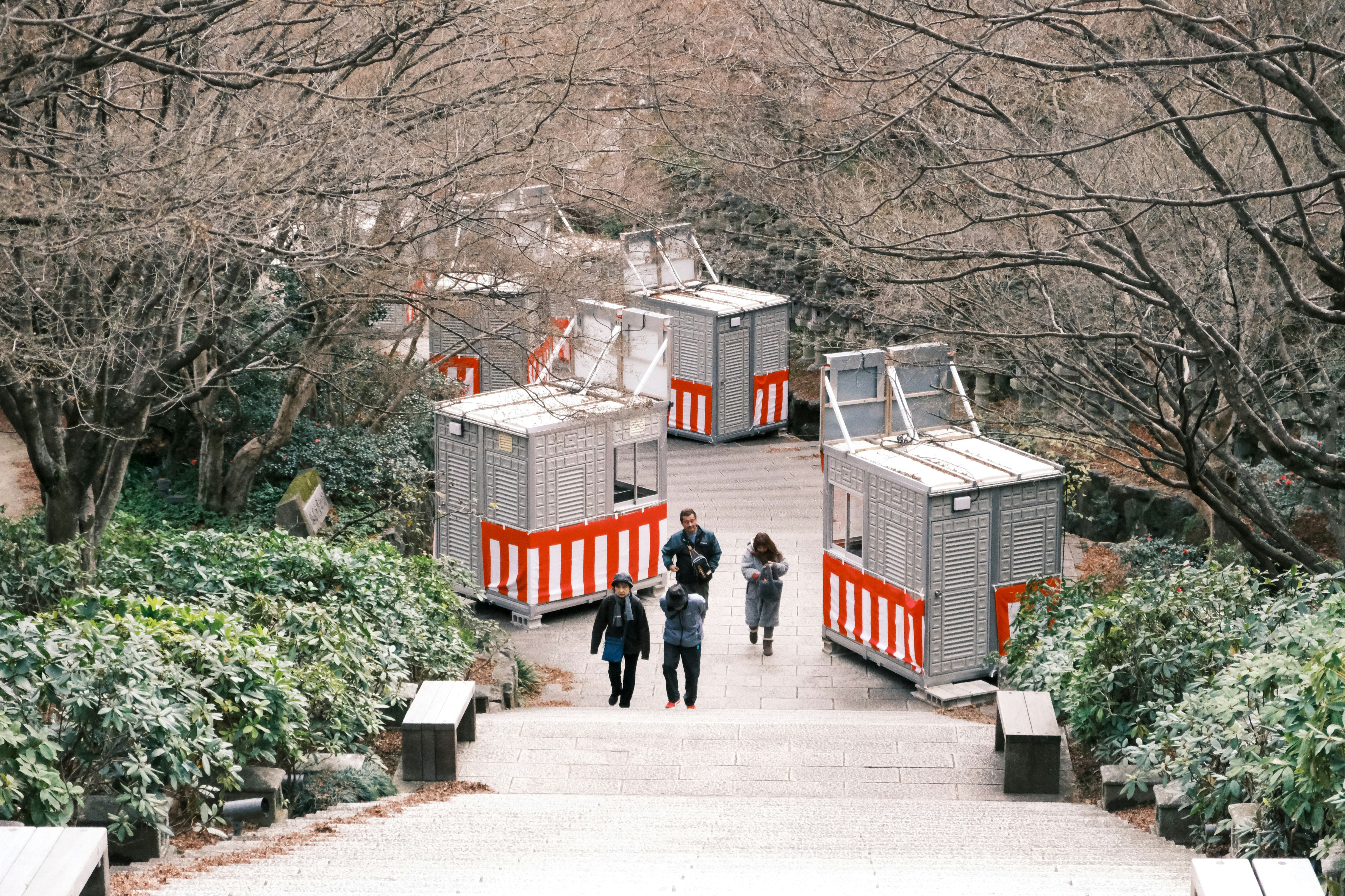 Four Pedestrians on a Tree-Lined Park Staircase Amid Red-and-White Striped Cabins