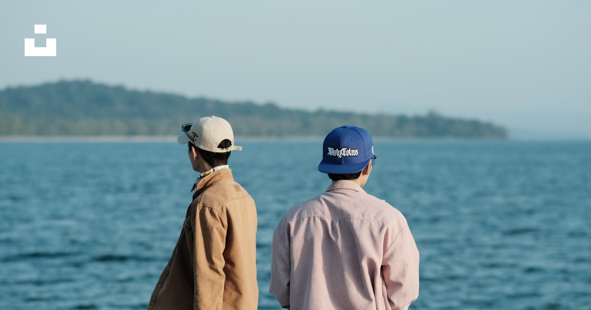 두 명의 남자가 물줄기 근처에 나란히 서 있다 사진 Unsplash의 무료 야구 모자 이미지