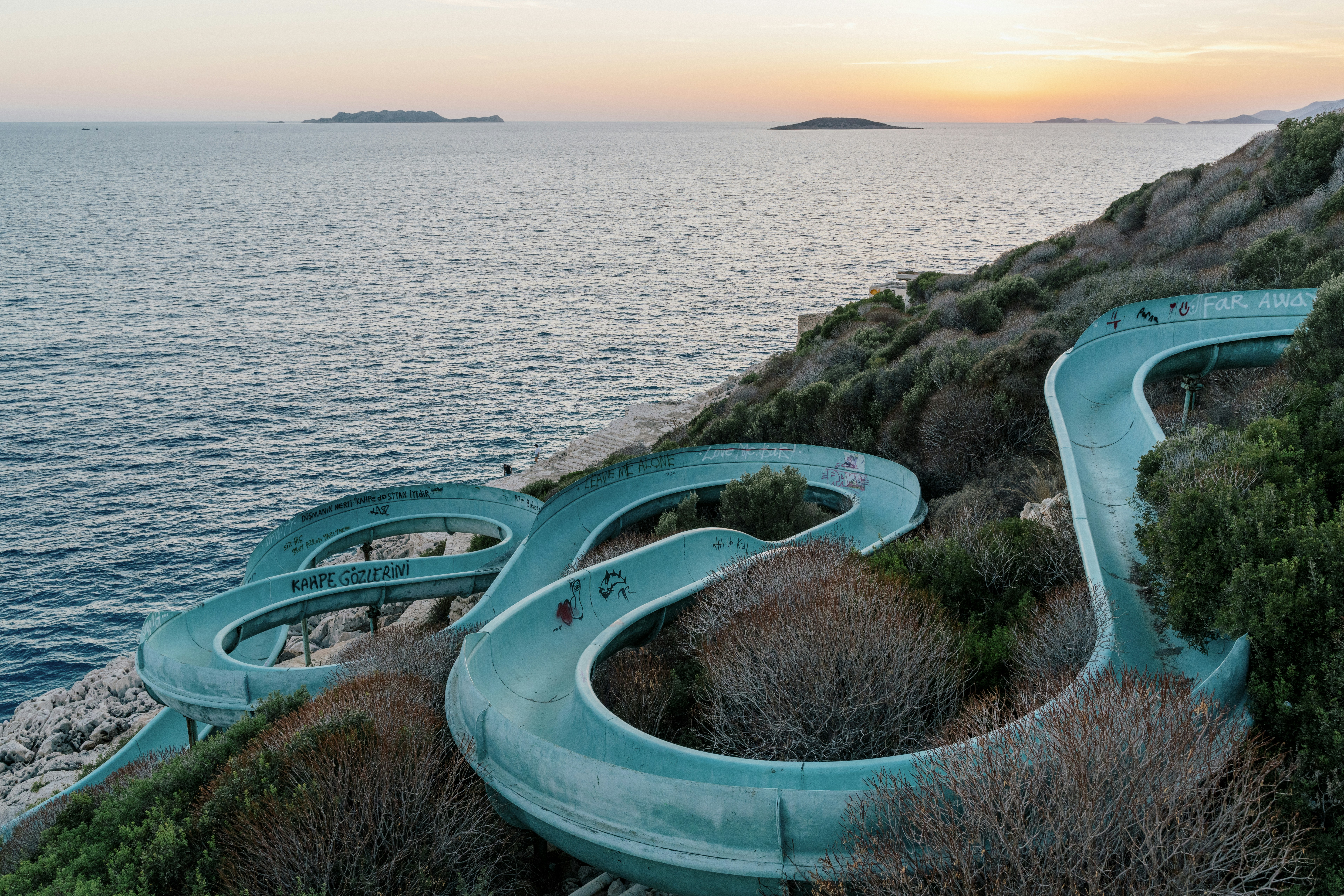 A water slide on the side of a cliff next to the ocean photo – Free ...