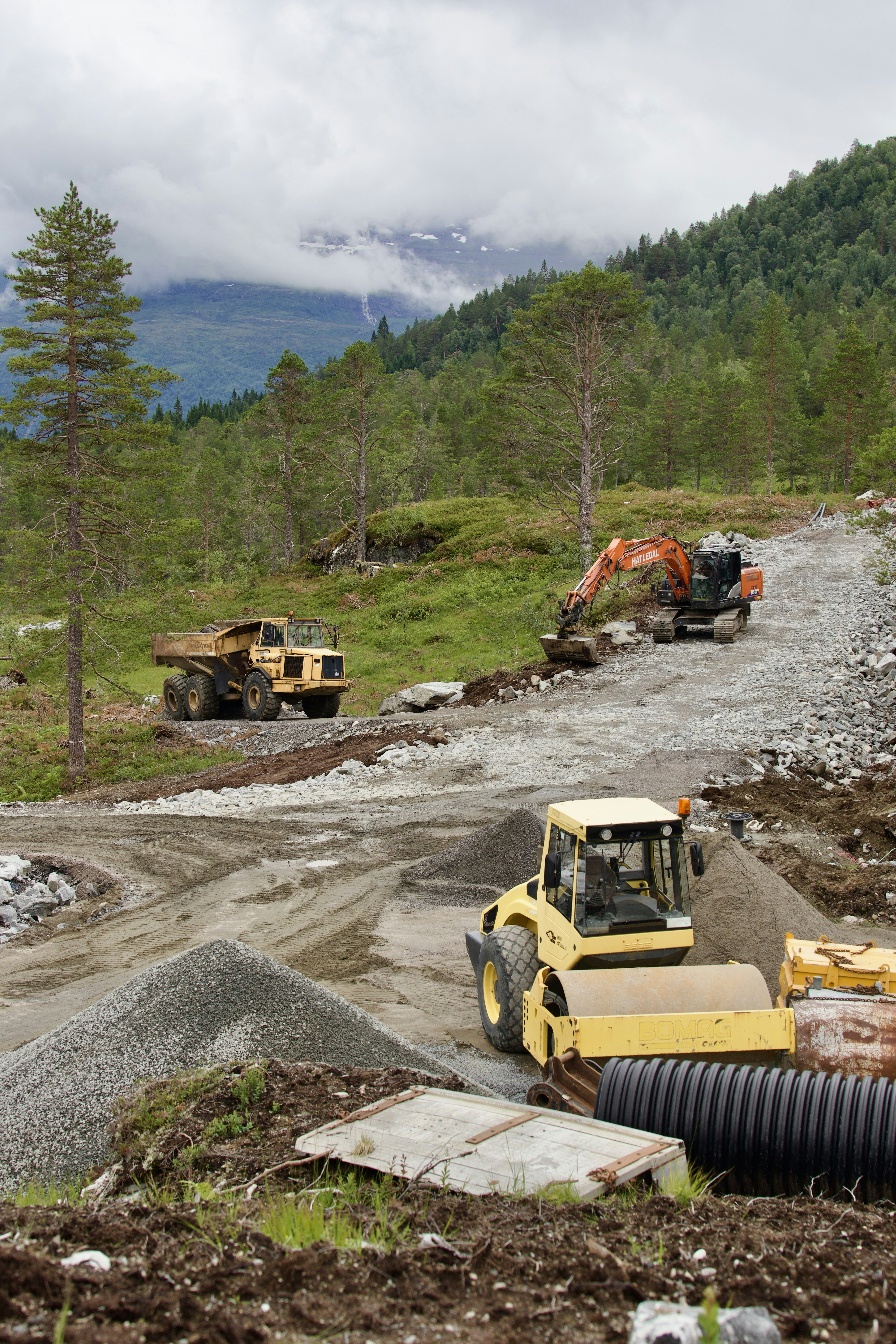 Mountain Worksite: Yellow Dump Truck and Orange Excavator Carving a Gravel Path
