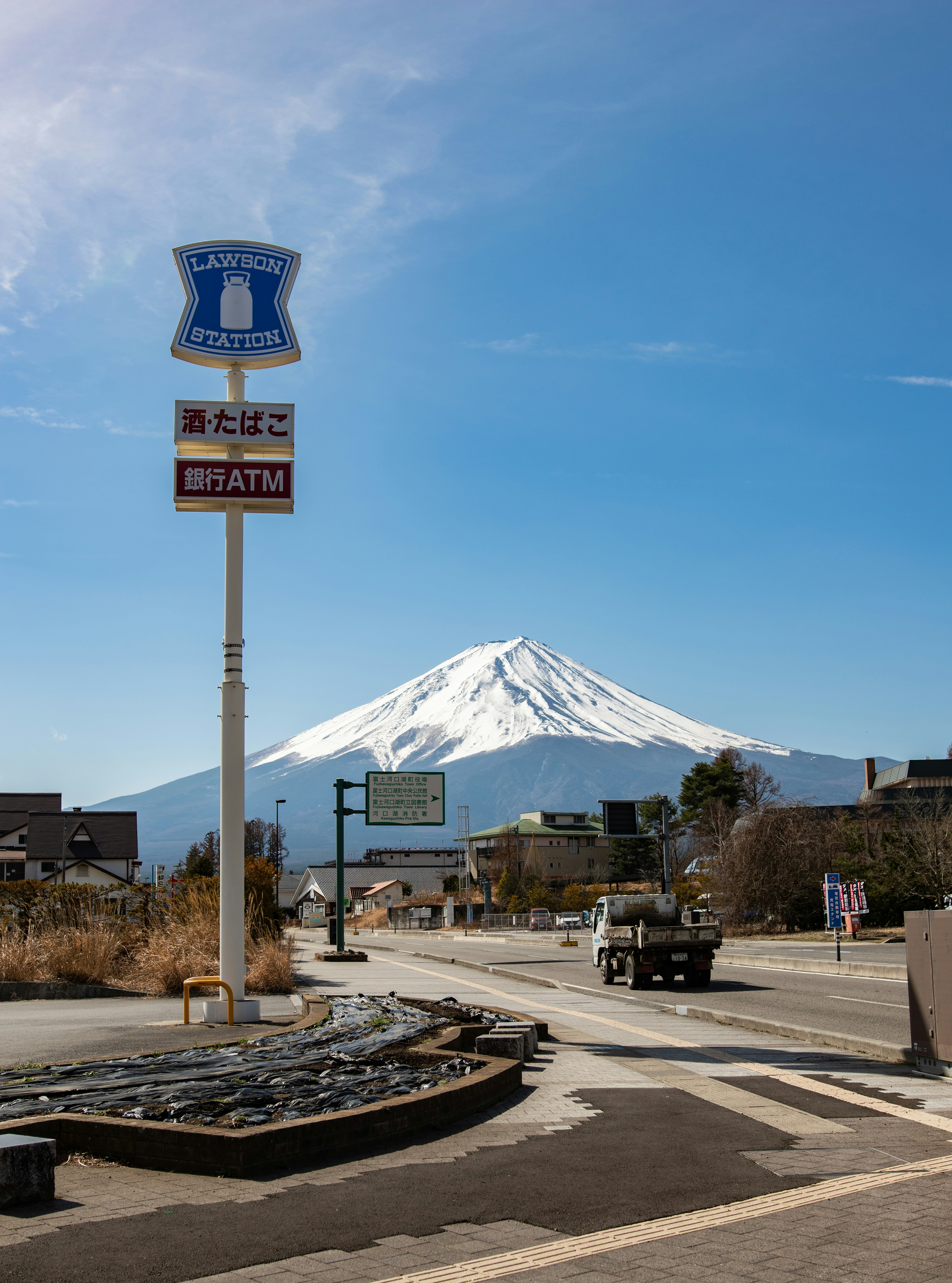 Lawson convenience store sign stands prominently in the foreground with Mount Fuji towering majestically in the background under a clear blue sky.