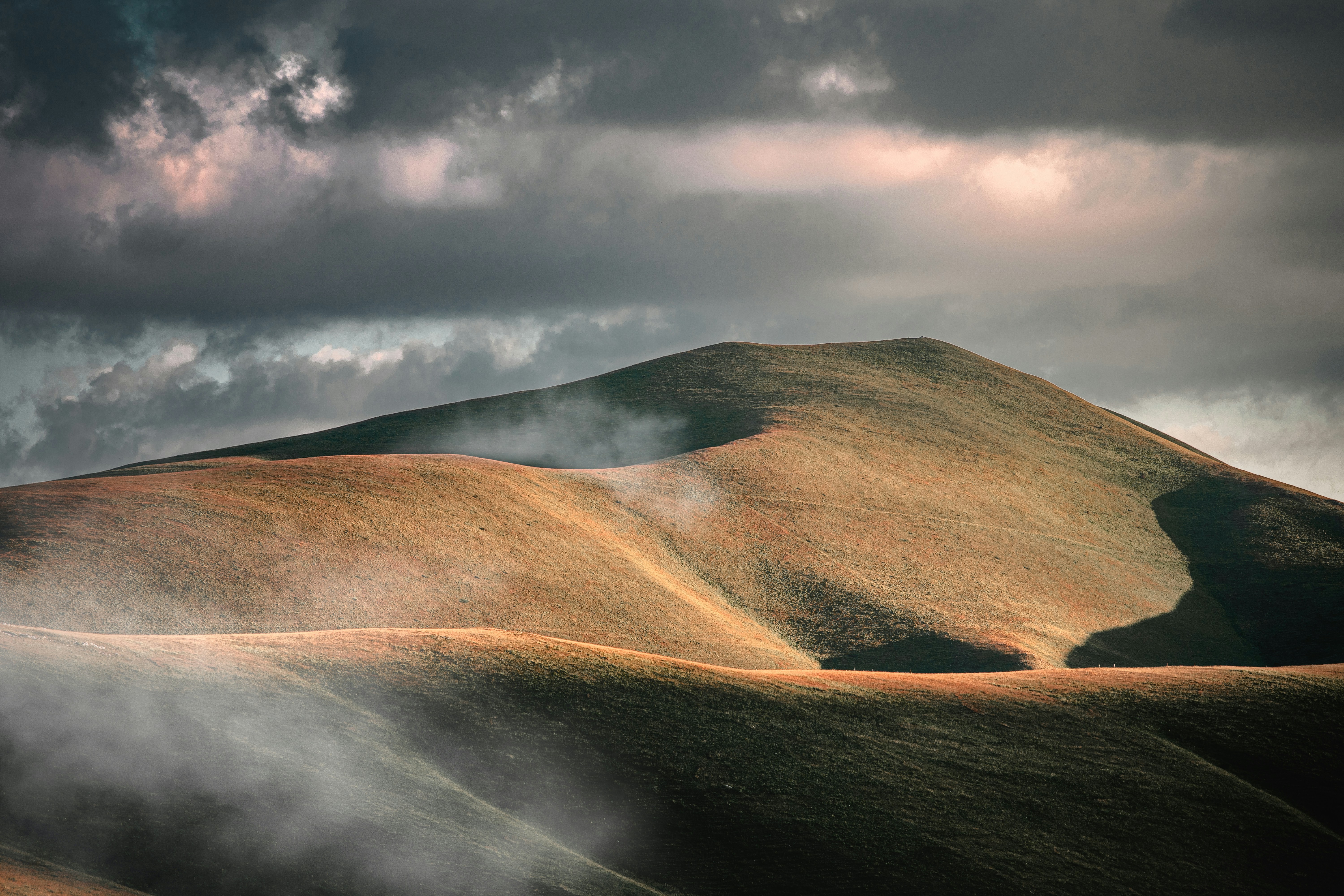 Rolling hills enveloped in mist under a dramatic cloudy sky.