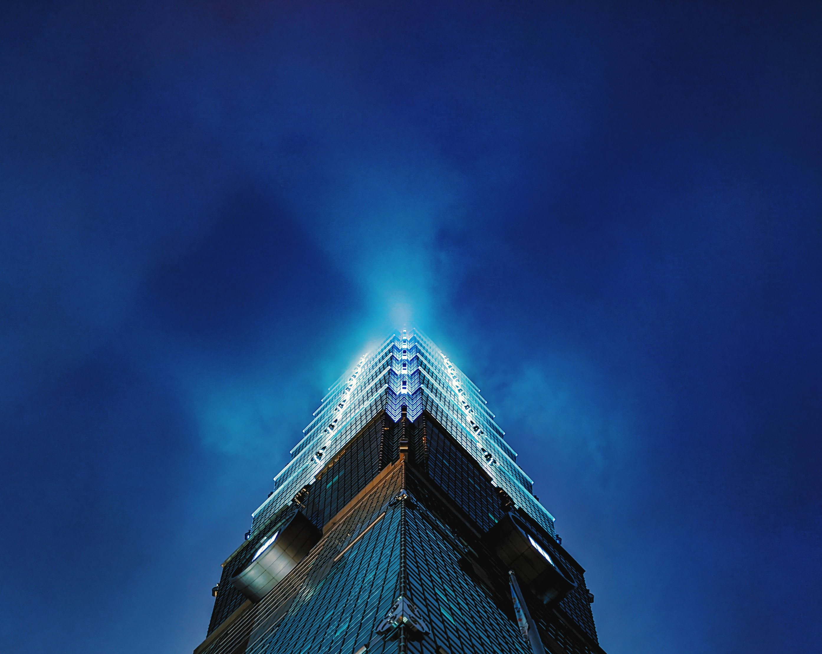 Night photograph of a glass skyscraper rising toward deep blue skies, its apex illuminated by a radiant glow.