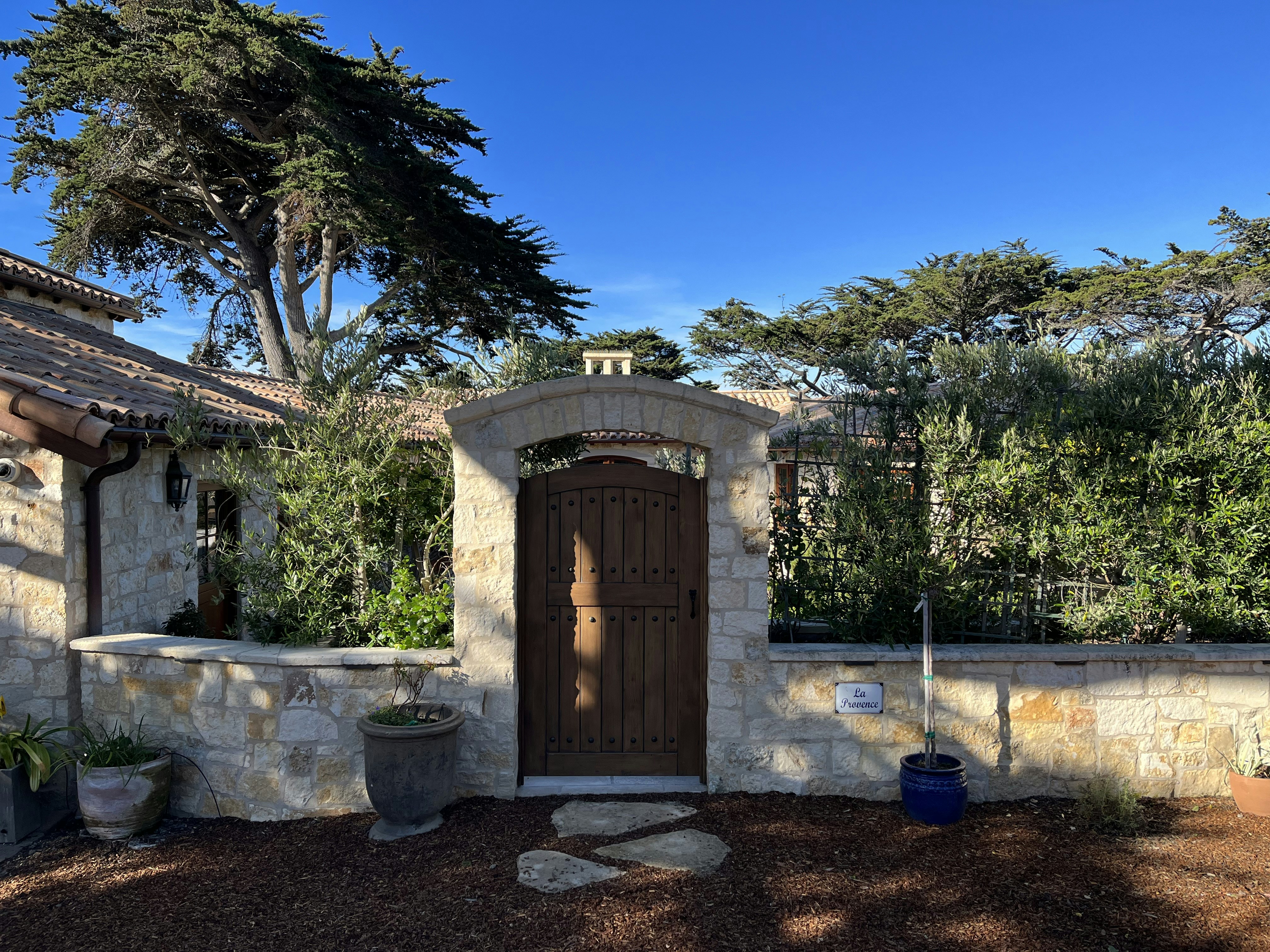 A beautifully crafted wooden door framed by stone walls and lush greenery, inviting visitors into a serene garden space.