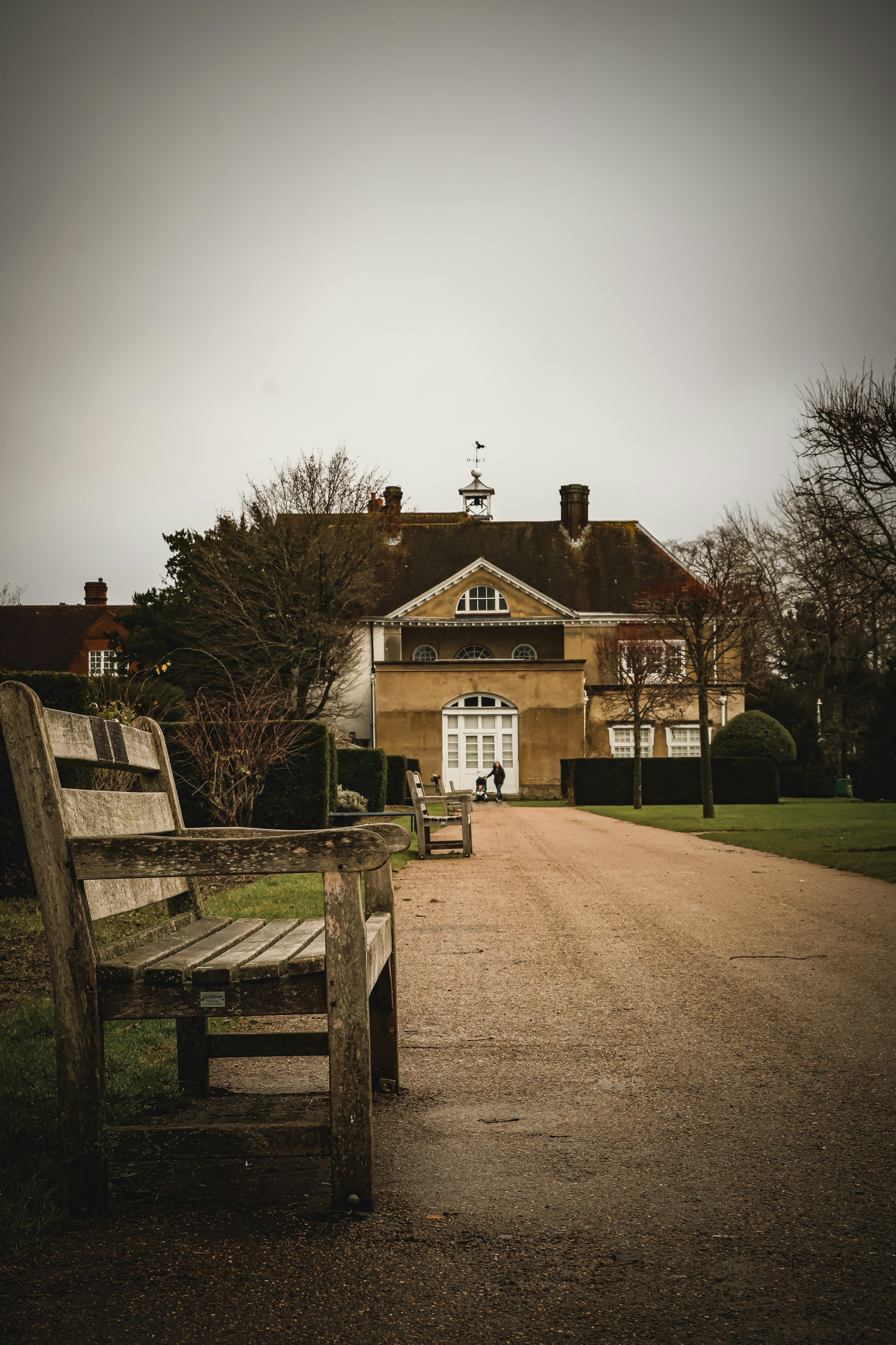 Gravel Promenade to a Weathered Manor: Benches, Trees, and a Quiet Entrance