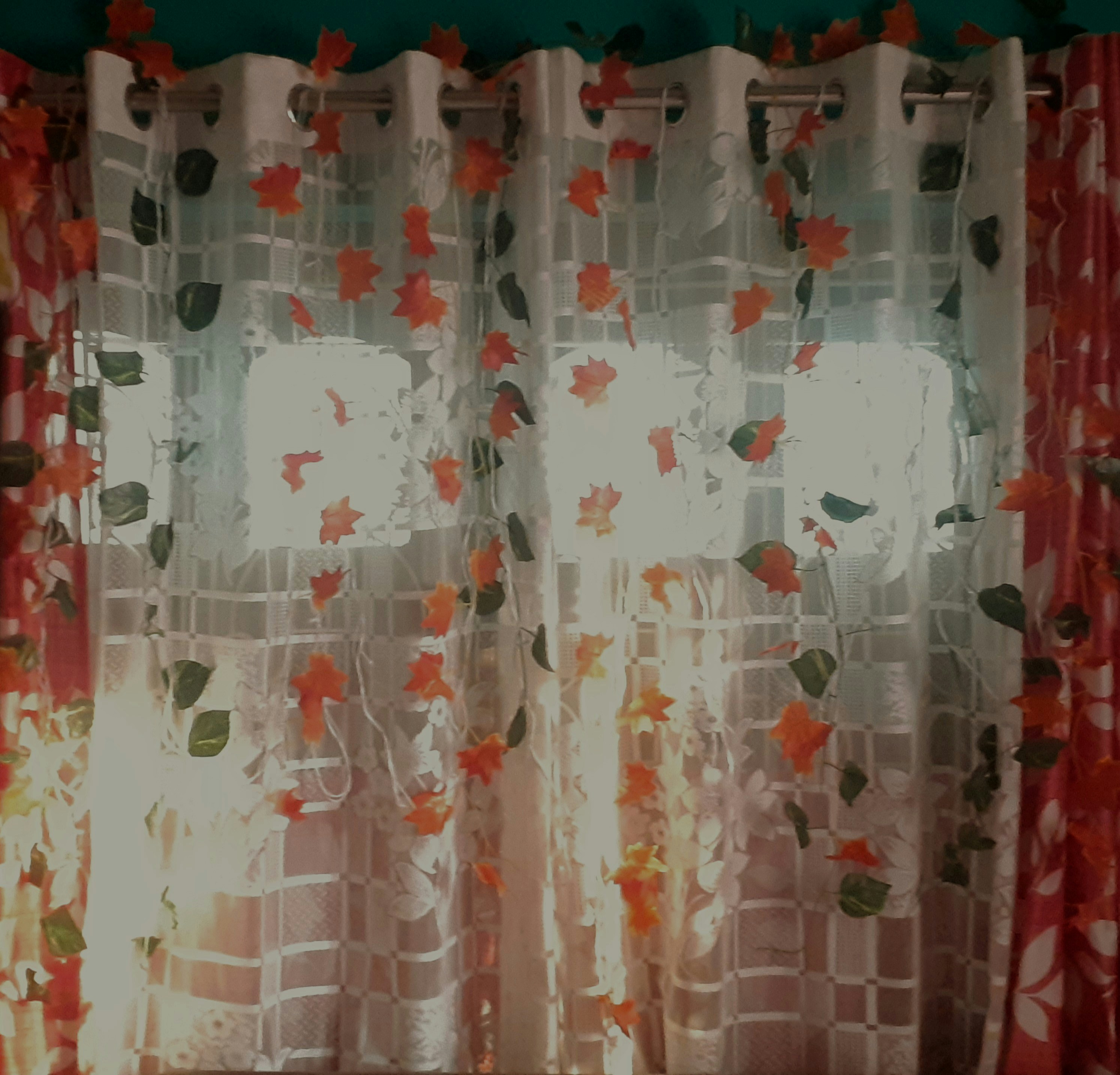 Sunlit window seen through sheer curtains with a leaf motif, casting a warm glow across the room.