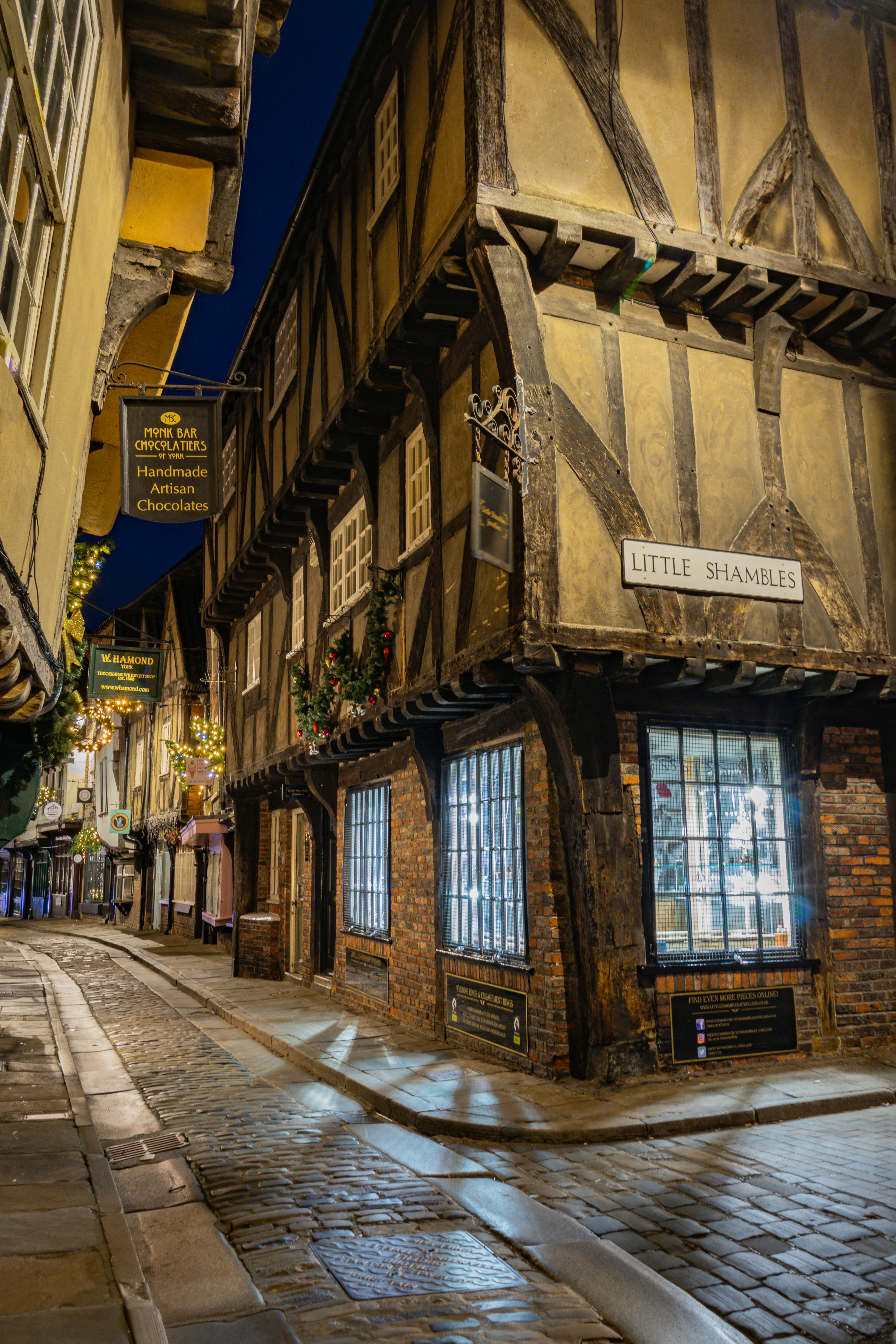 Cobblestone street with timber-framed buildings adorned with festive lights in a European city at night.