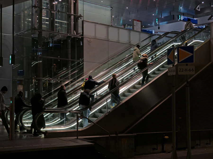 Several travelers ride a brightly lit escalator inside a modern transit terminal at night, with glass walls and reflective surfaces surrounding them.