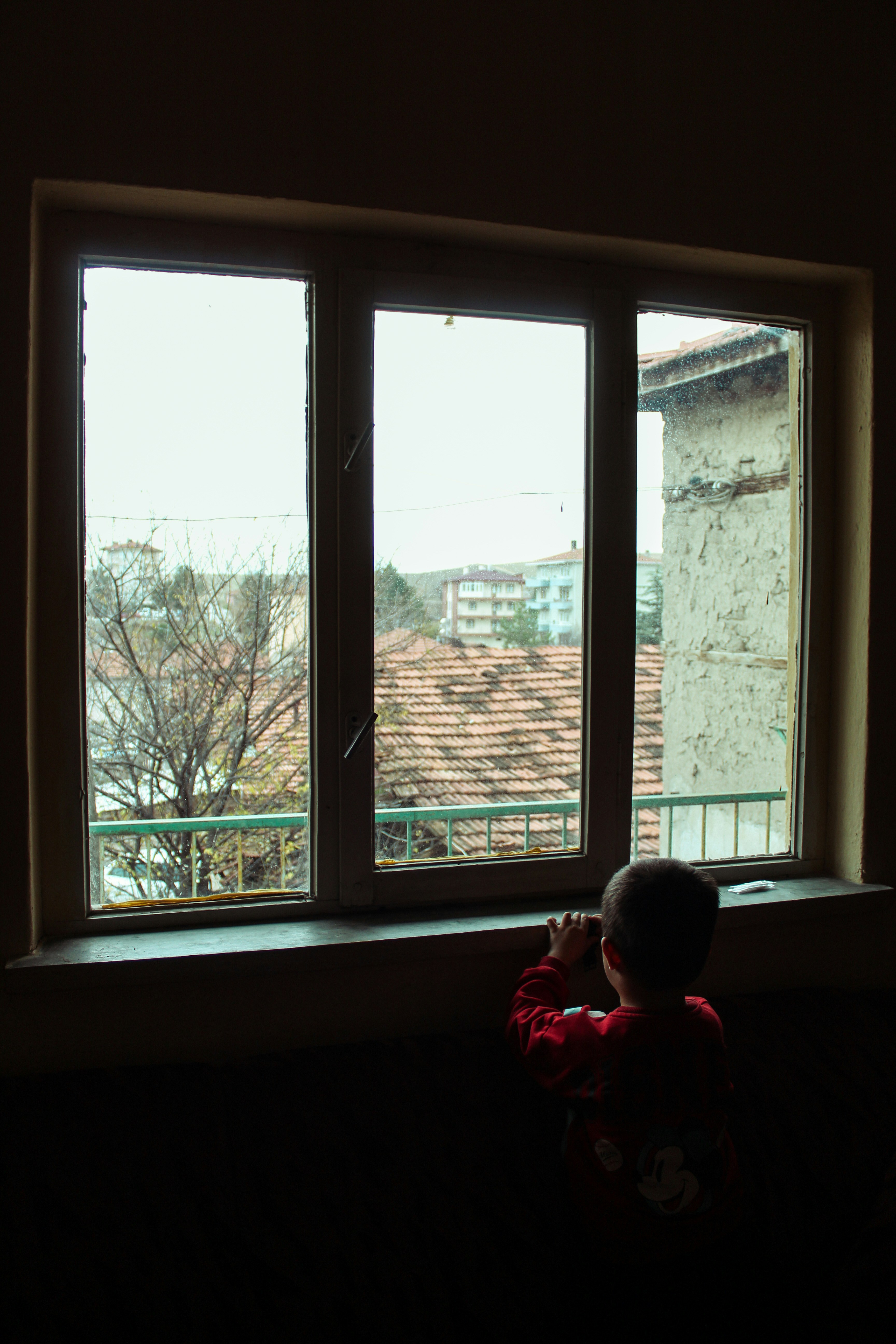 A young child looking out a window at a city photo – Free Window Image ...