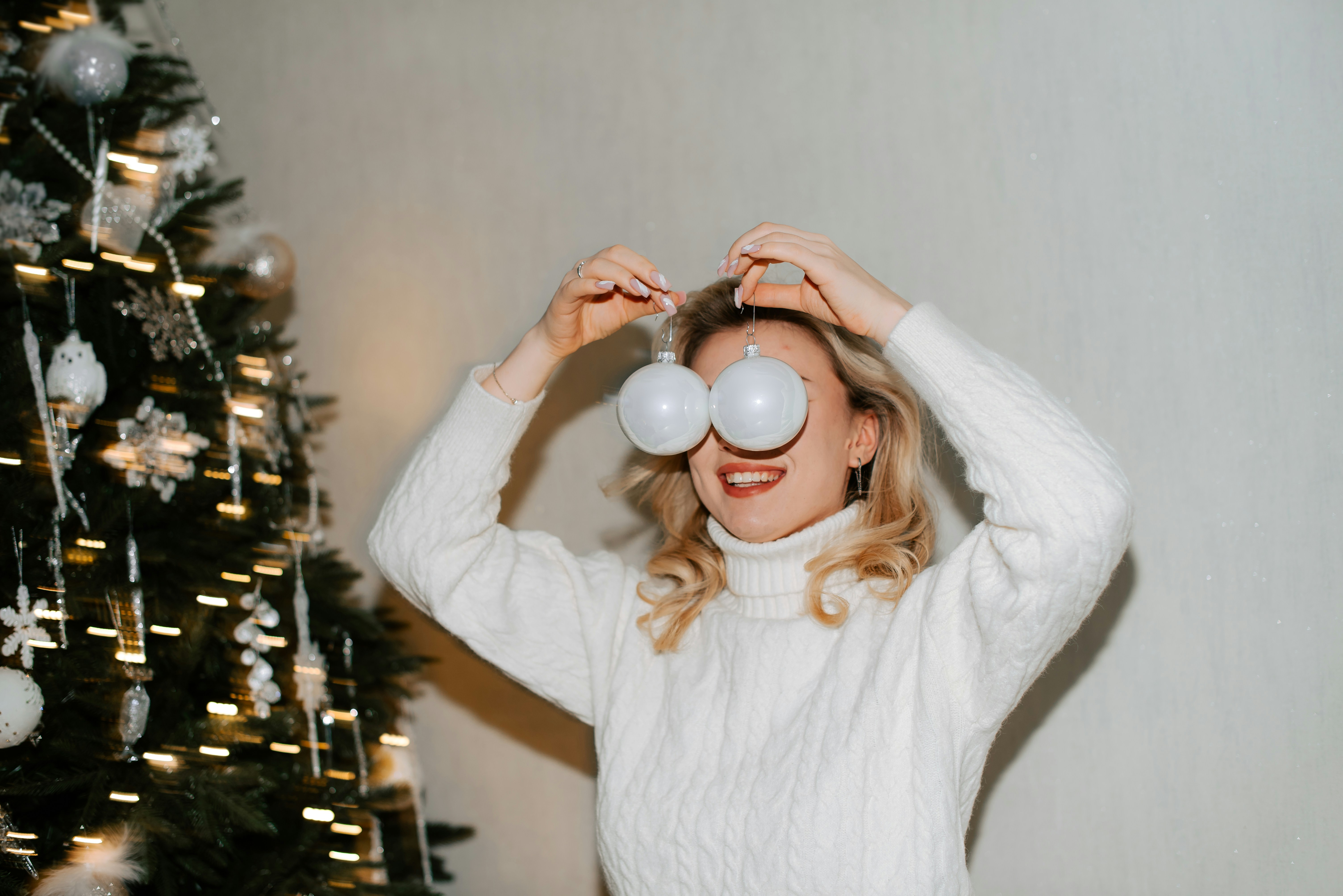 A woman in a white sweater holding two white balls over her eyes photo ...