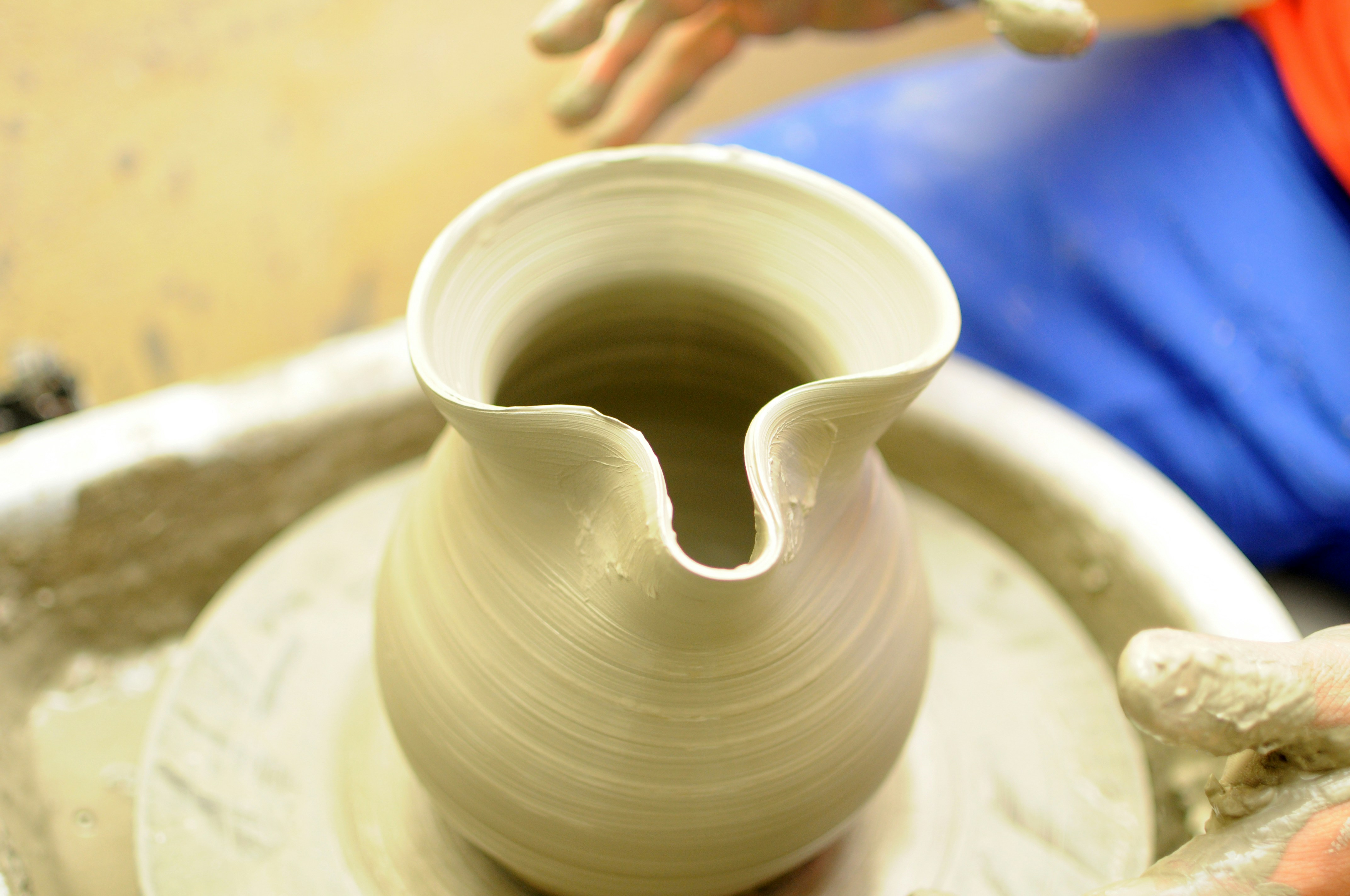 Foto ravvicinata di mani che lavorano l'argilla modellando sul tornio o in maniera statica. Foto scattata durante un corso di lavorazione artigianale della ceramica con metodi tradizionali. Close-up photo of hands working clay, either shaping it on a pottery wheel or in a static manner. The photo was taken during a traditional ceramic crafting course.