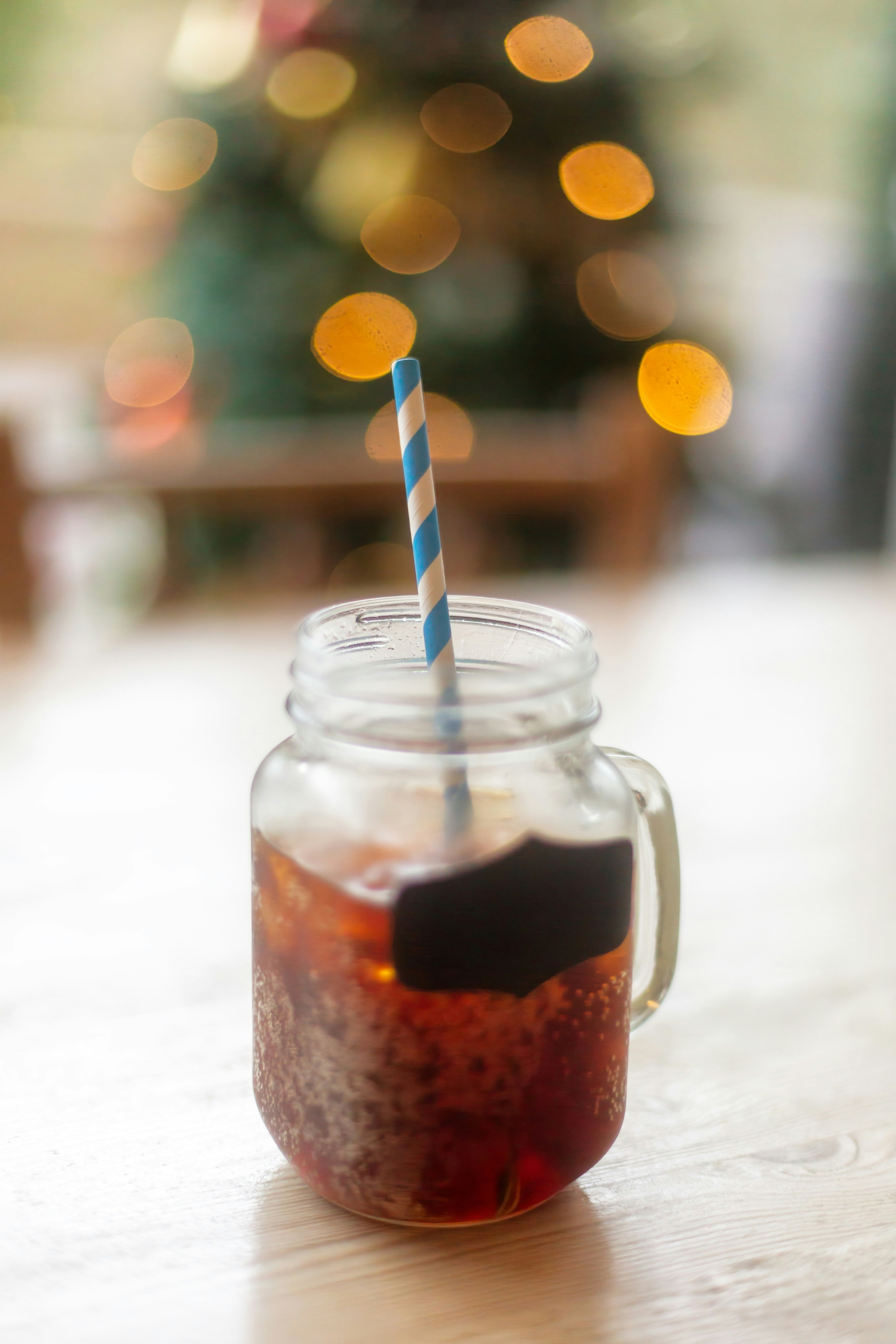 A cold drink in a jar glass with a straw, in a cafe, with a soft focus Christmas tree in the background.