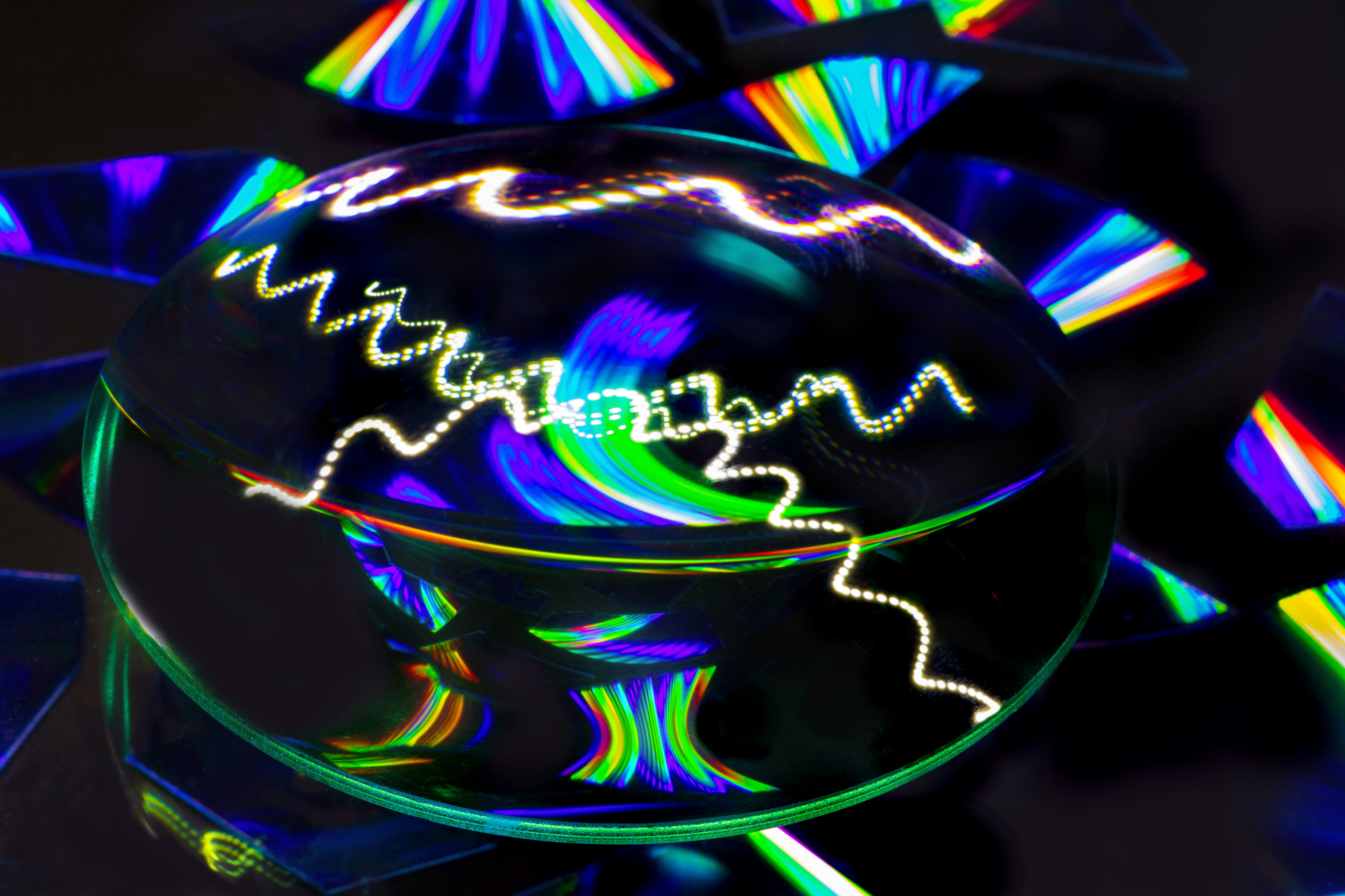 Colorful light patterns refract through a bi-convex lens above CD fragments.