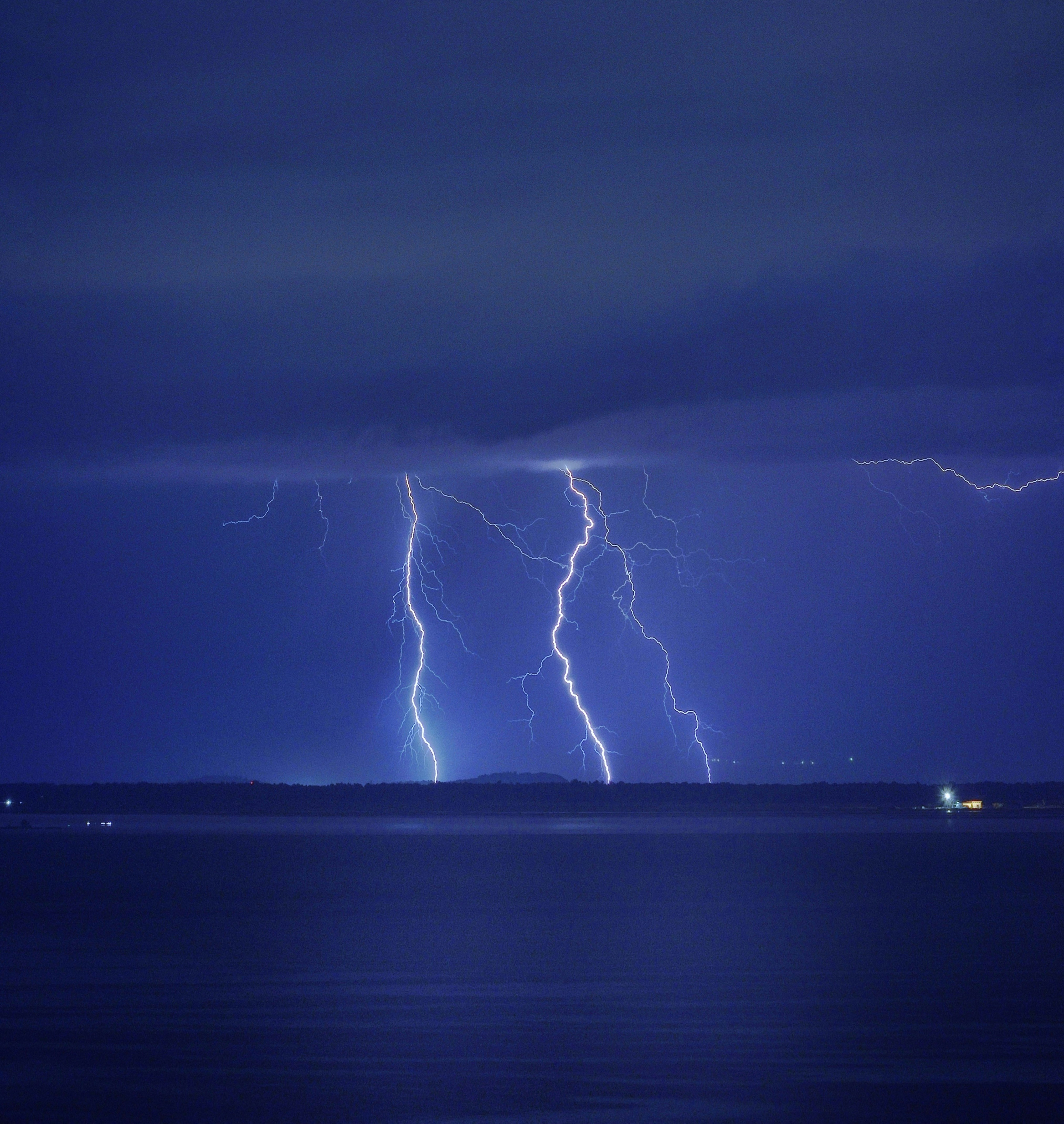 A couple of lightning strikes over a body of water photo – Free Storm ...