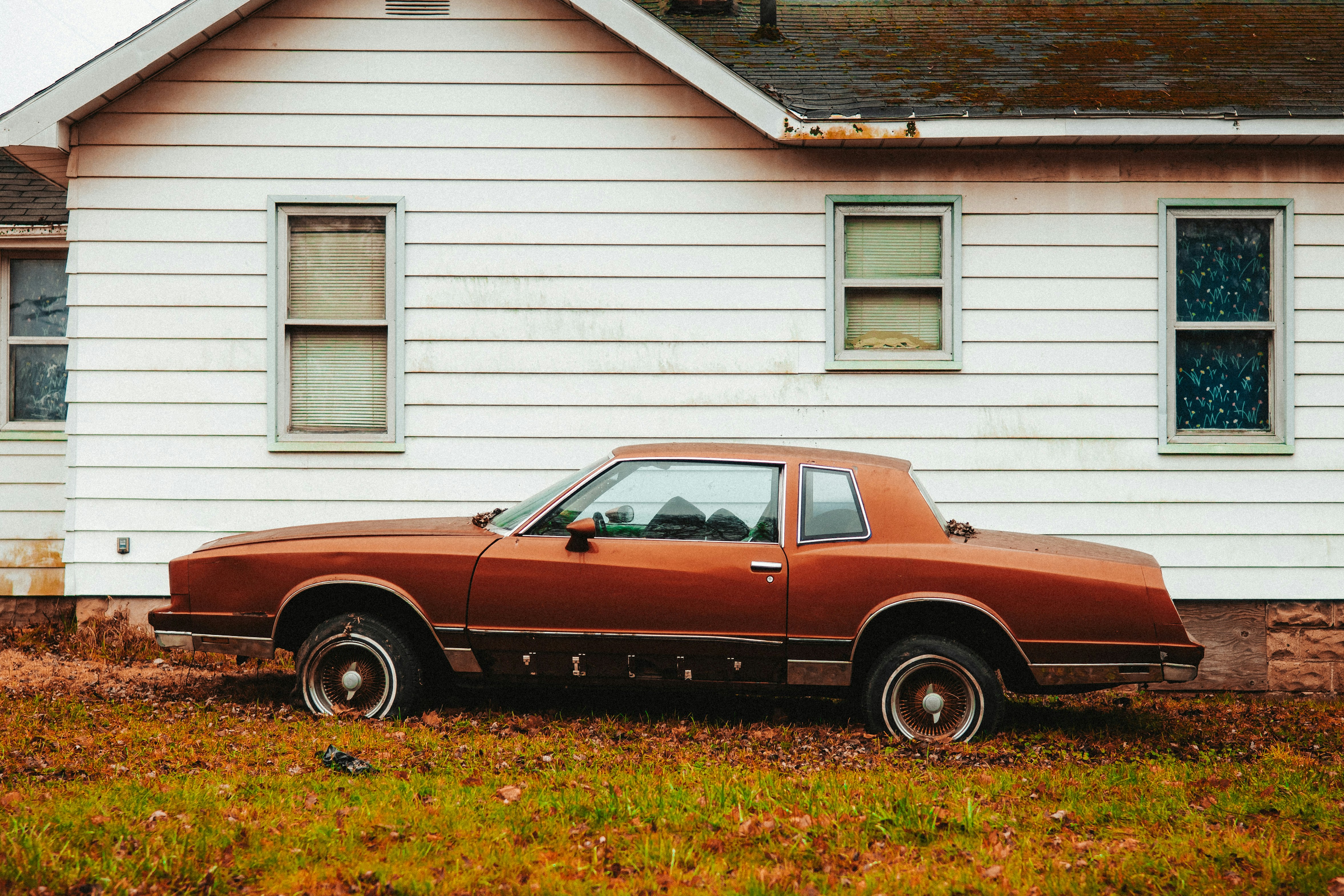 Suburban relic: An orange vintage coupe beside a weathered white house