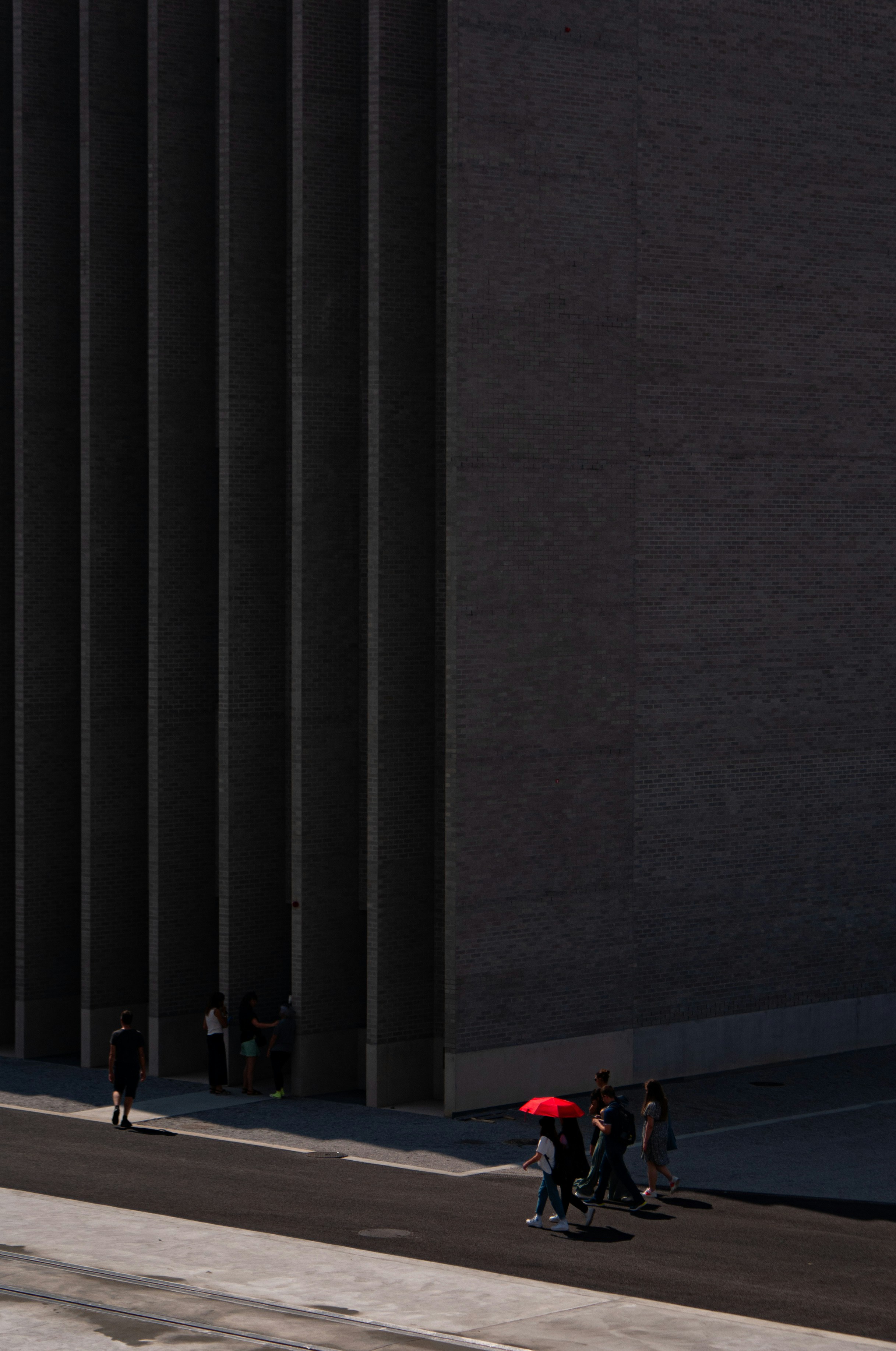 A group of people walking down a street next to a tall building photo ...