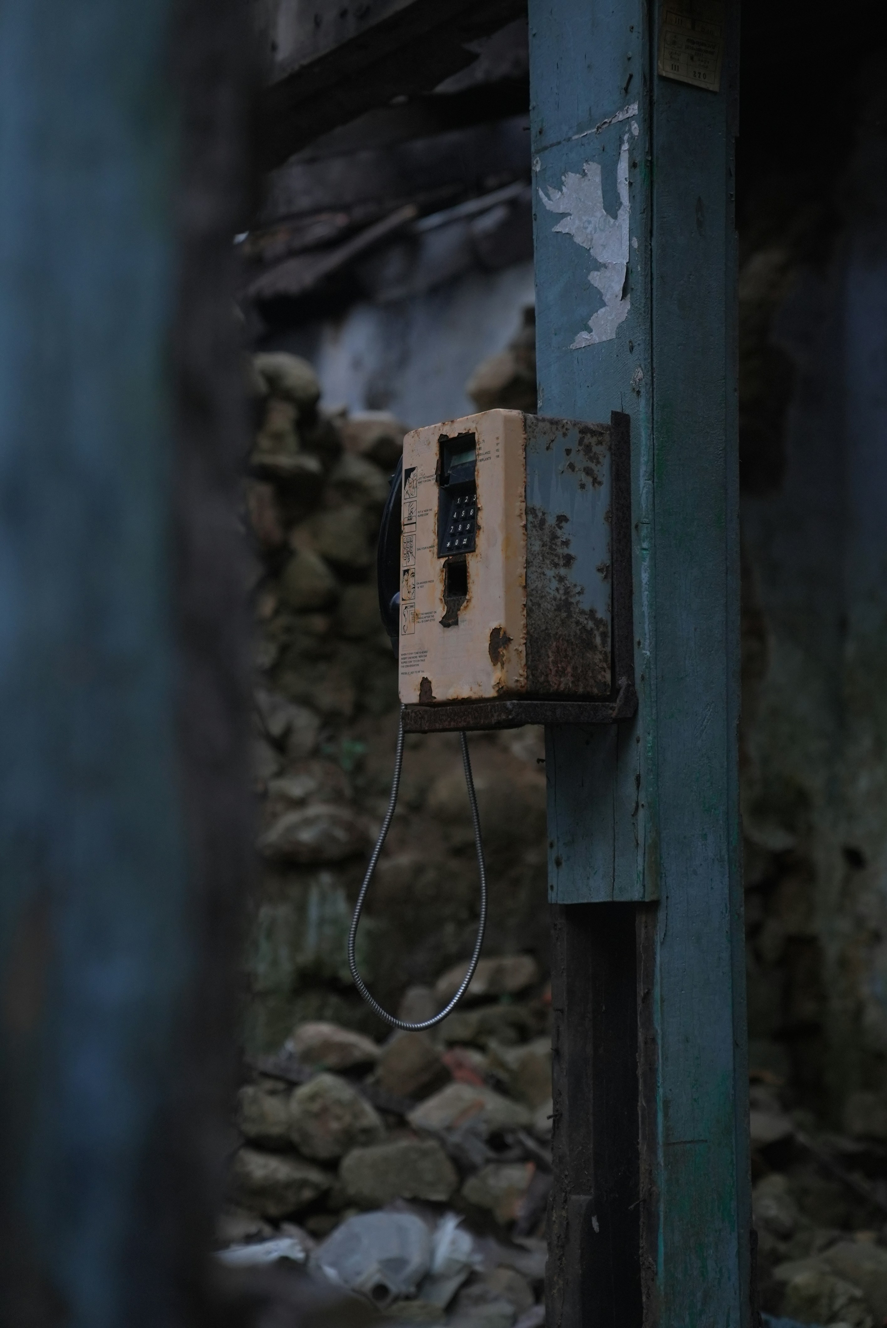 Rust, Post, and Silence: A Weathered Payphone in a Derelict Yard