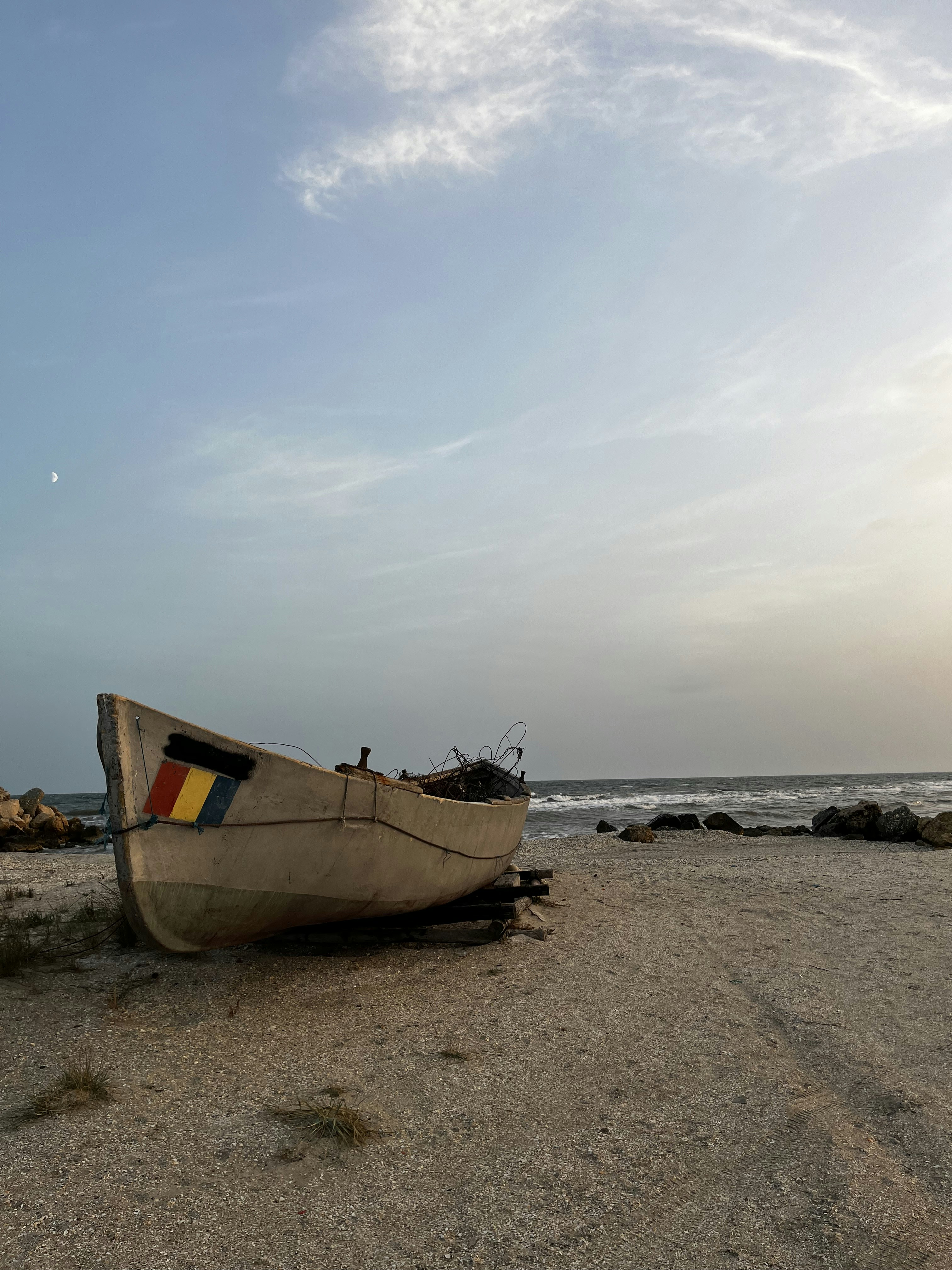 Weathered Boat Resting on a Pebble Beach Beneath a Dusk Sky and a Crescent Moon