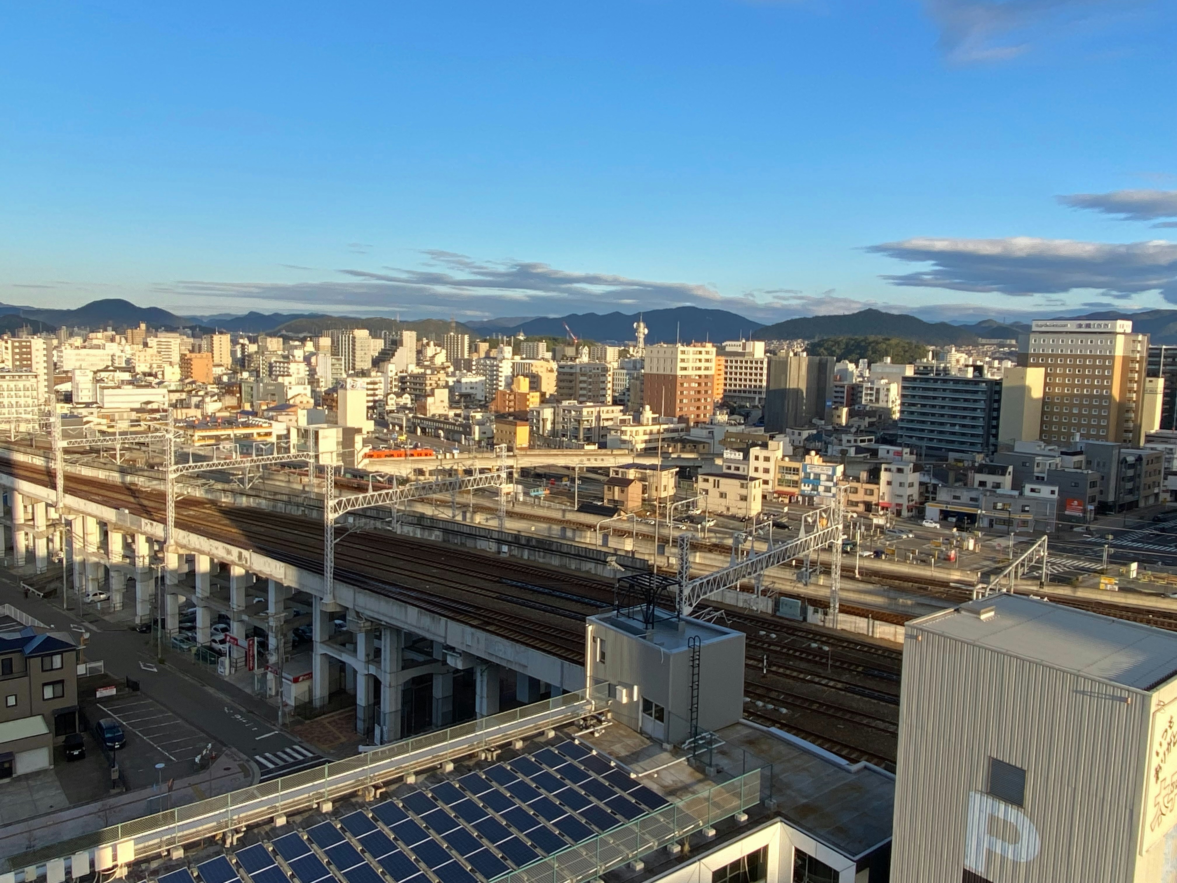 Cityscape featuring elevated train tracks with a distant mountain backdrop under a clear blue sky.