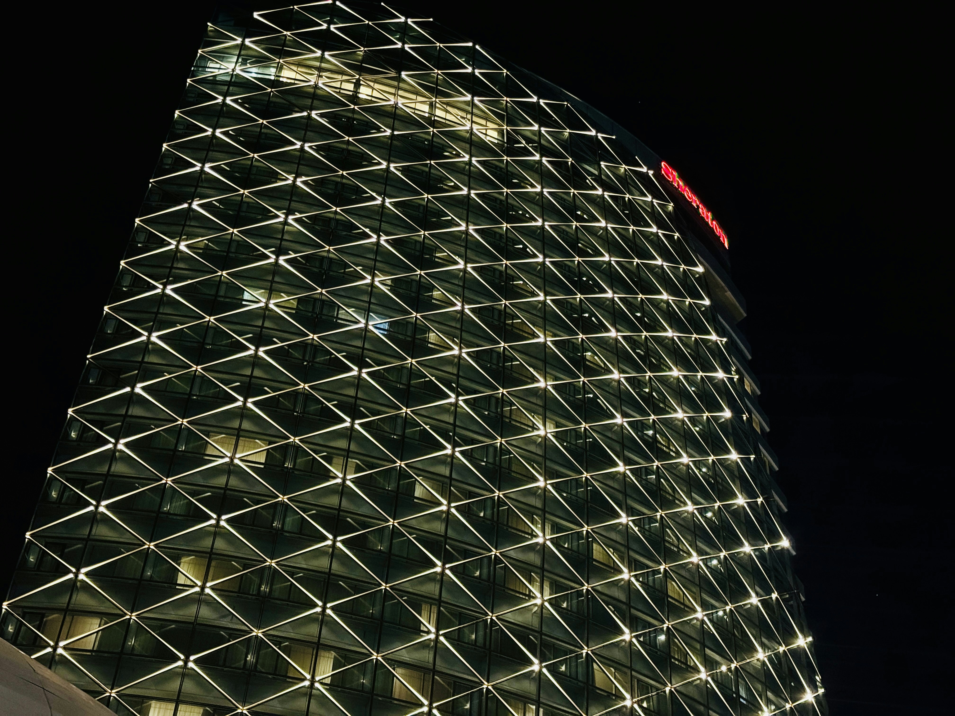 Luminous Diamond Grid: Night Facade of a Curved Glass Tower