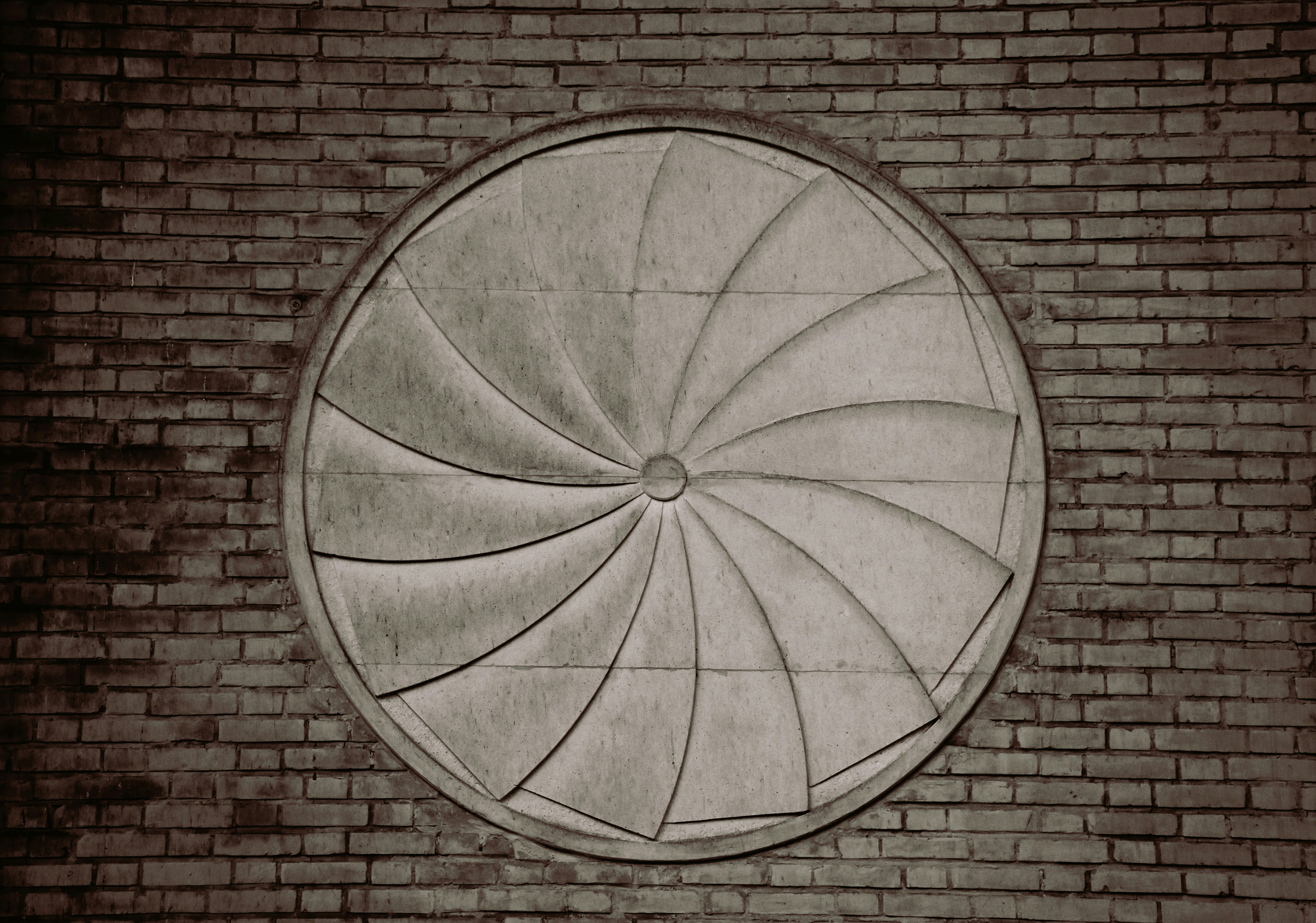 Circular vent at brick wall: radial spokes framing an architectural lens