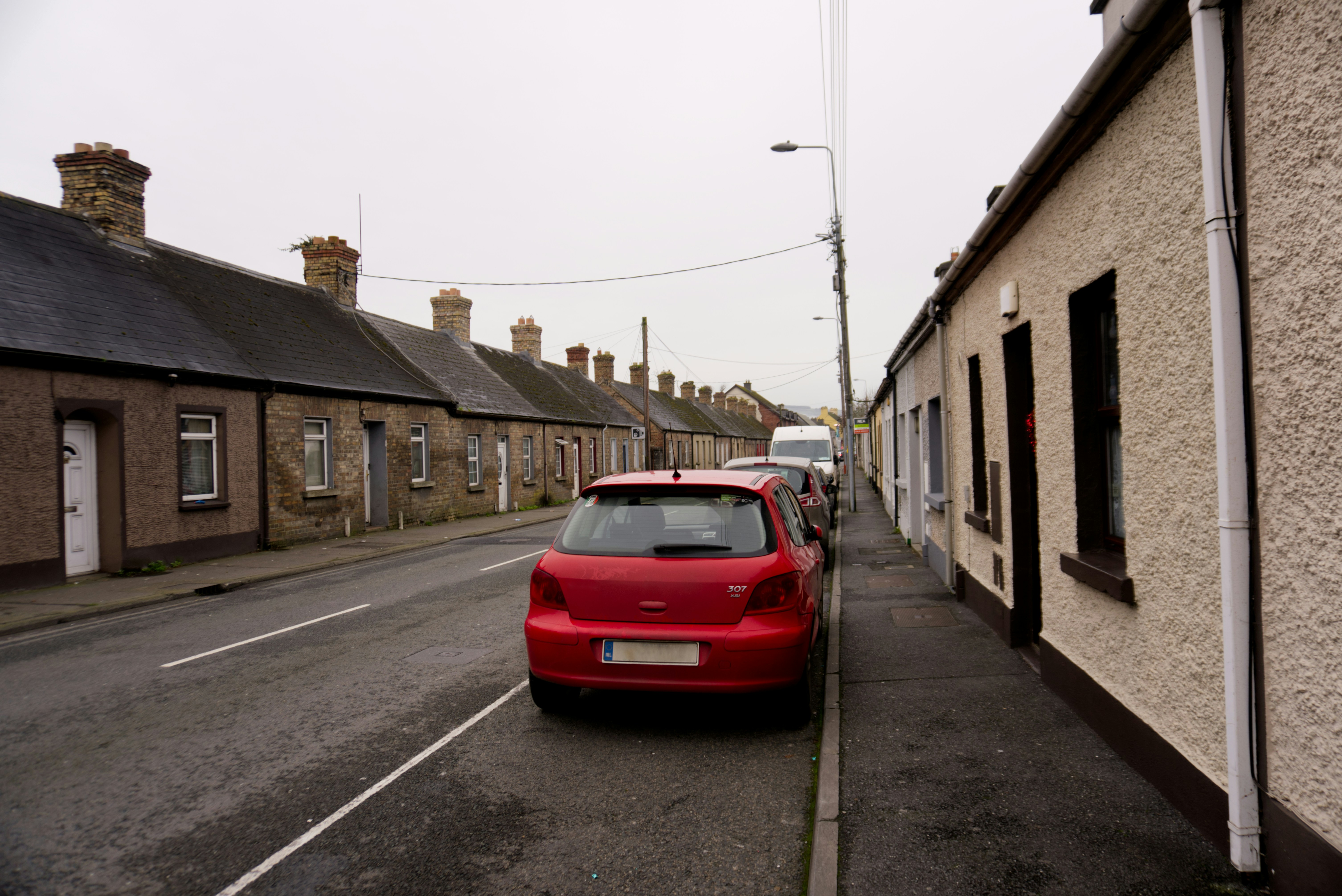 Red hatchback anchoring a quiet street in overcast townscape