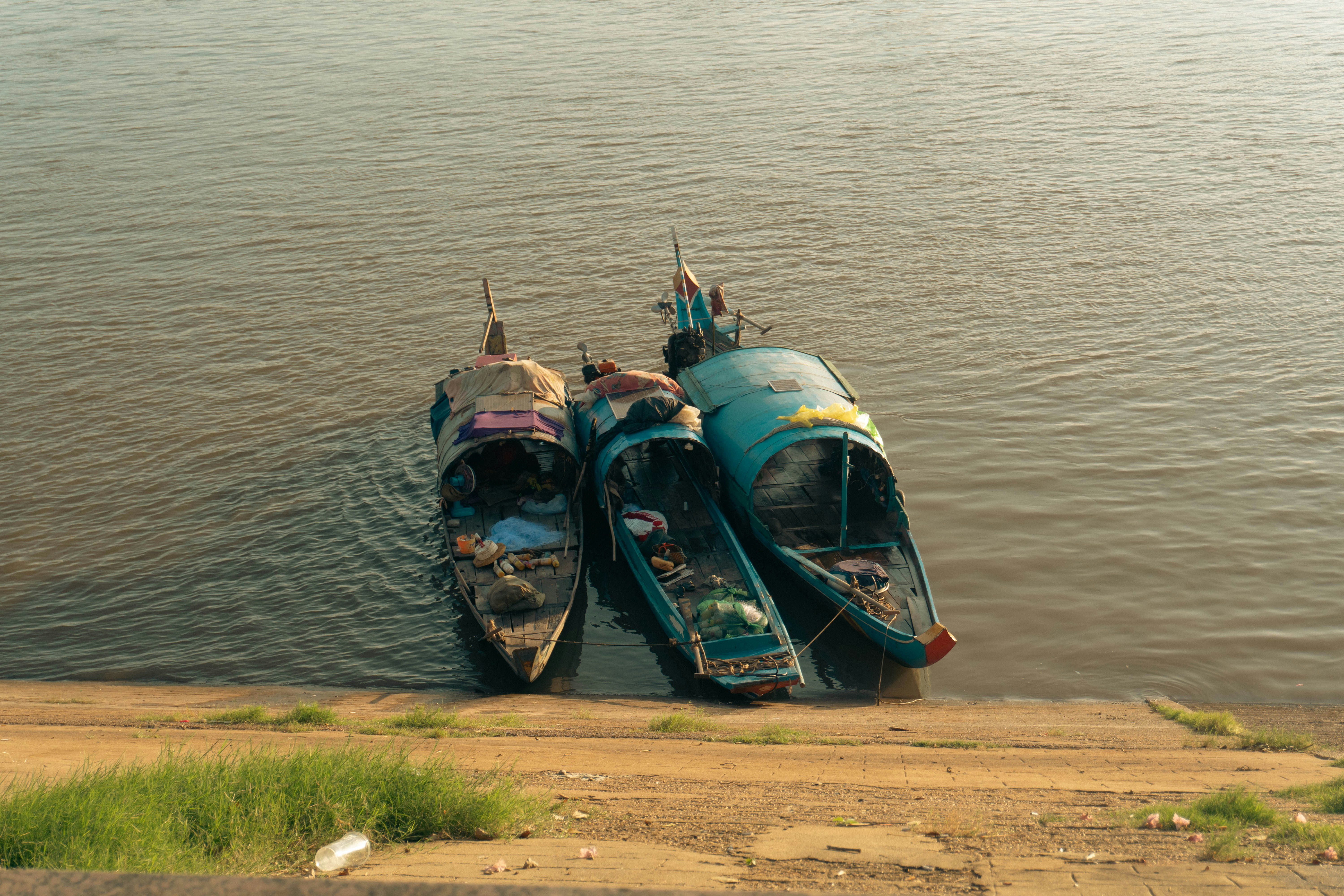 Three Weathered Boats Moored Along a Quiet Riverbank in Warm Light