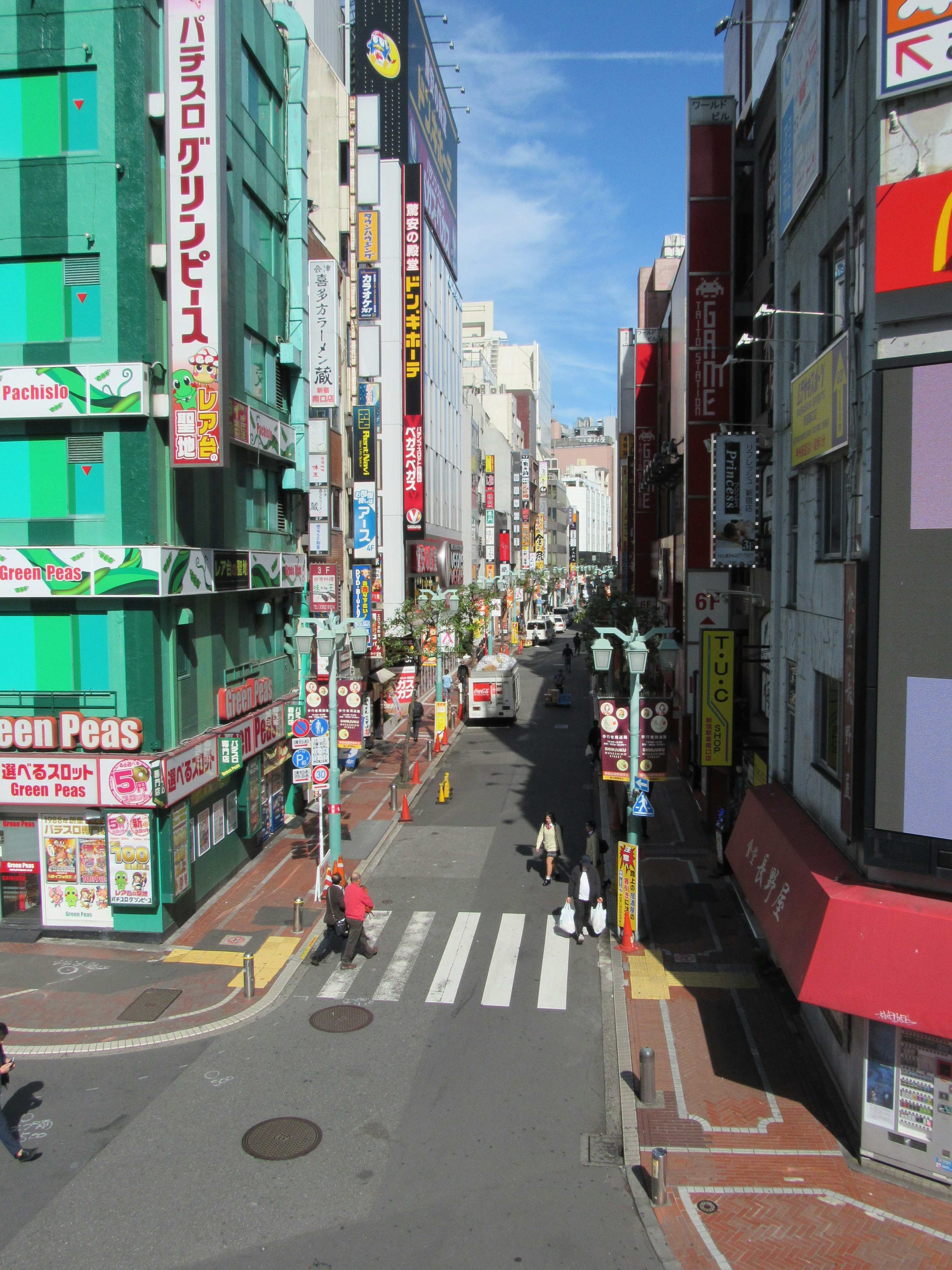 Vivid city street photo lined with colorful signs and tall buildings, leading pedestrians and a crosswalk toward a distant vanishing point.