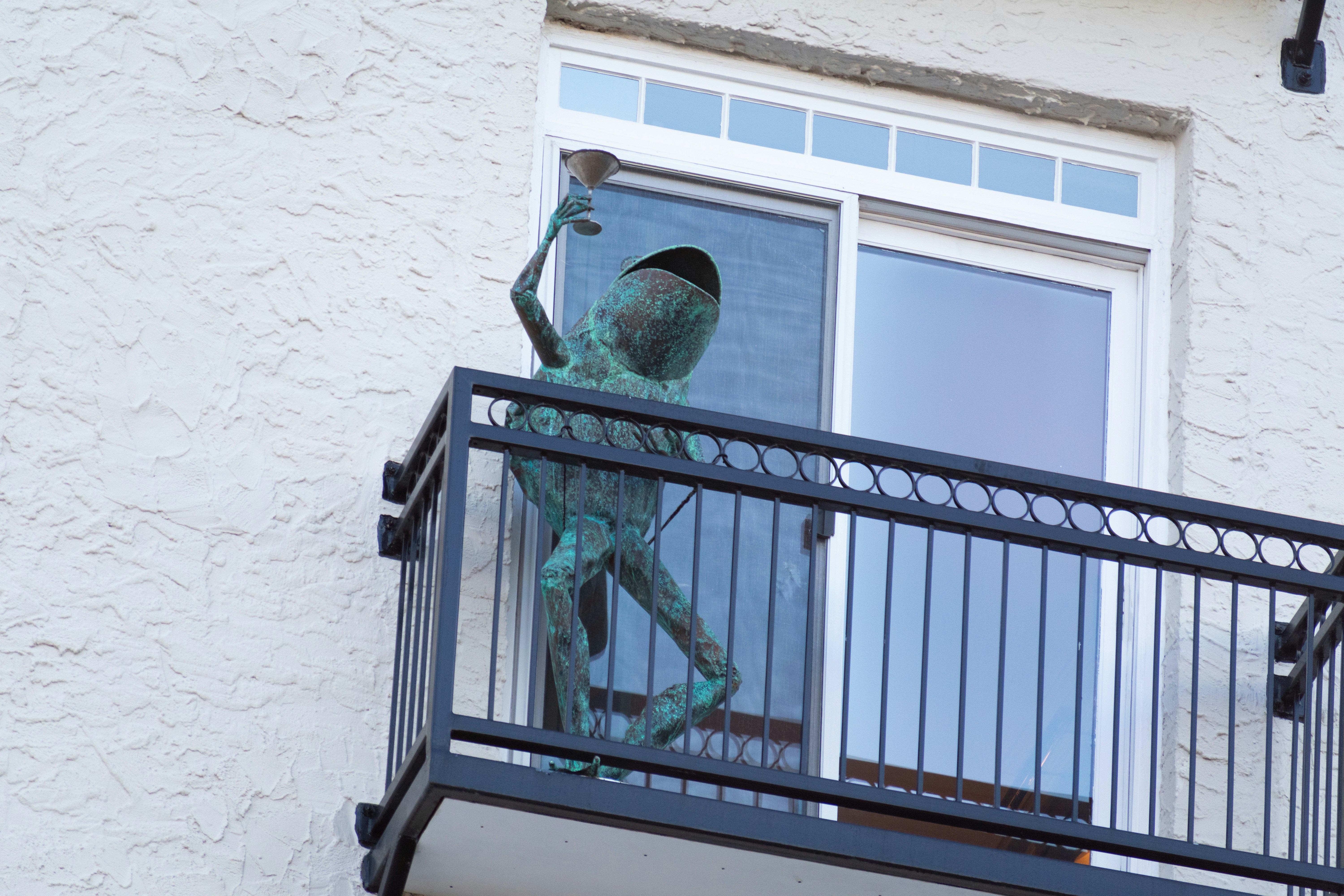 Bronze statue of a figure playfully posed on a balcony railing.