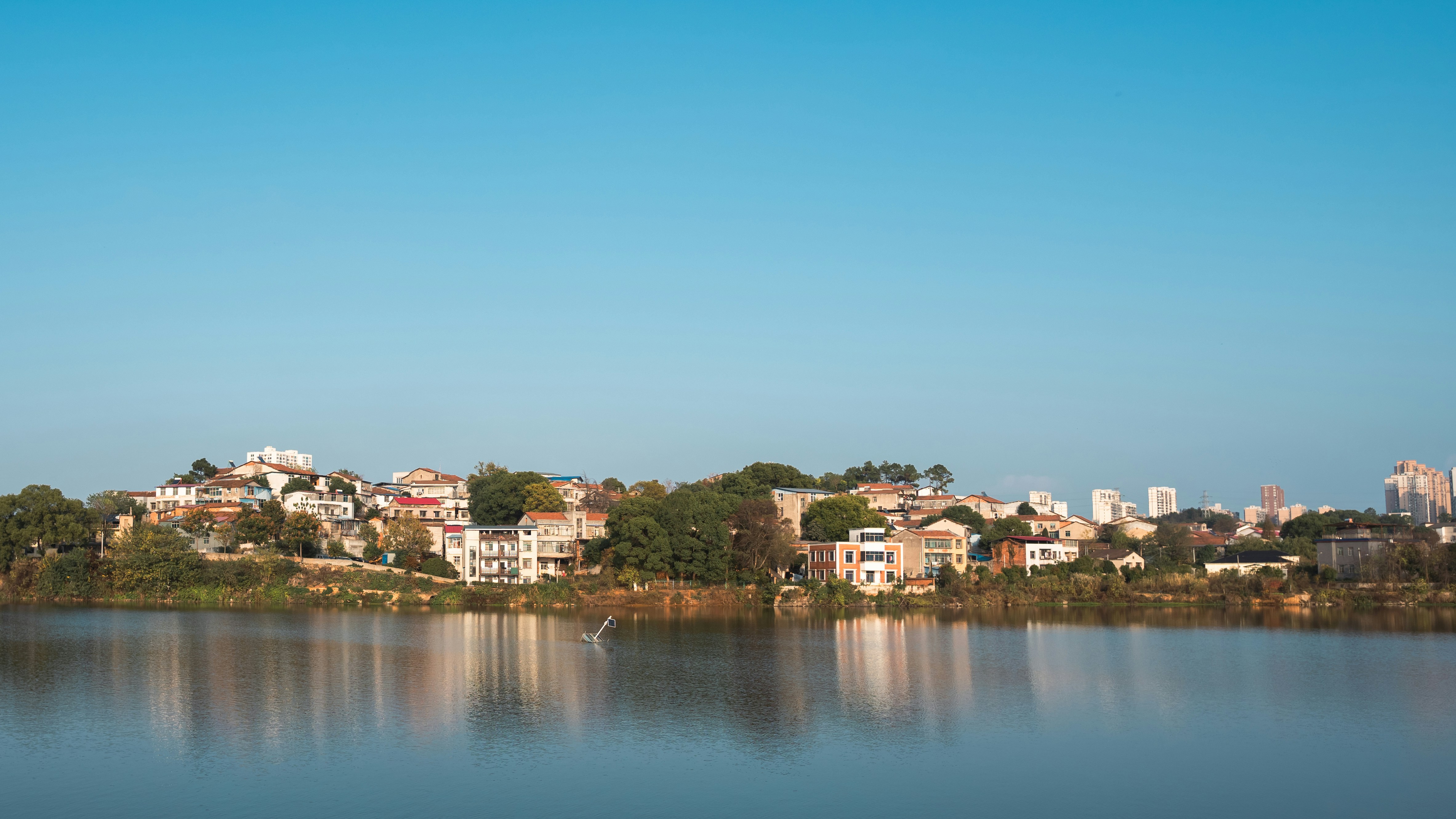 Calm water reflecting a distant city skyline under a clear blue sky.