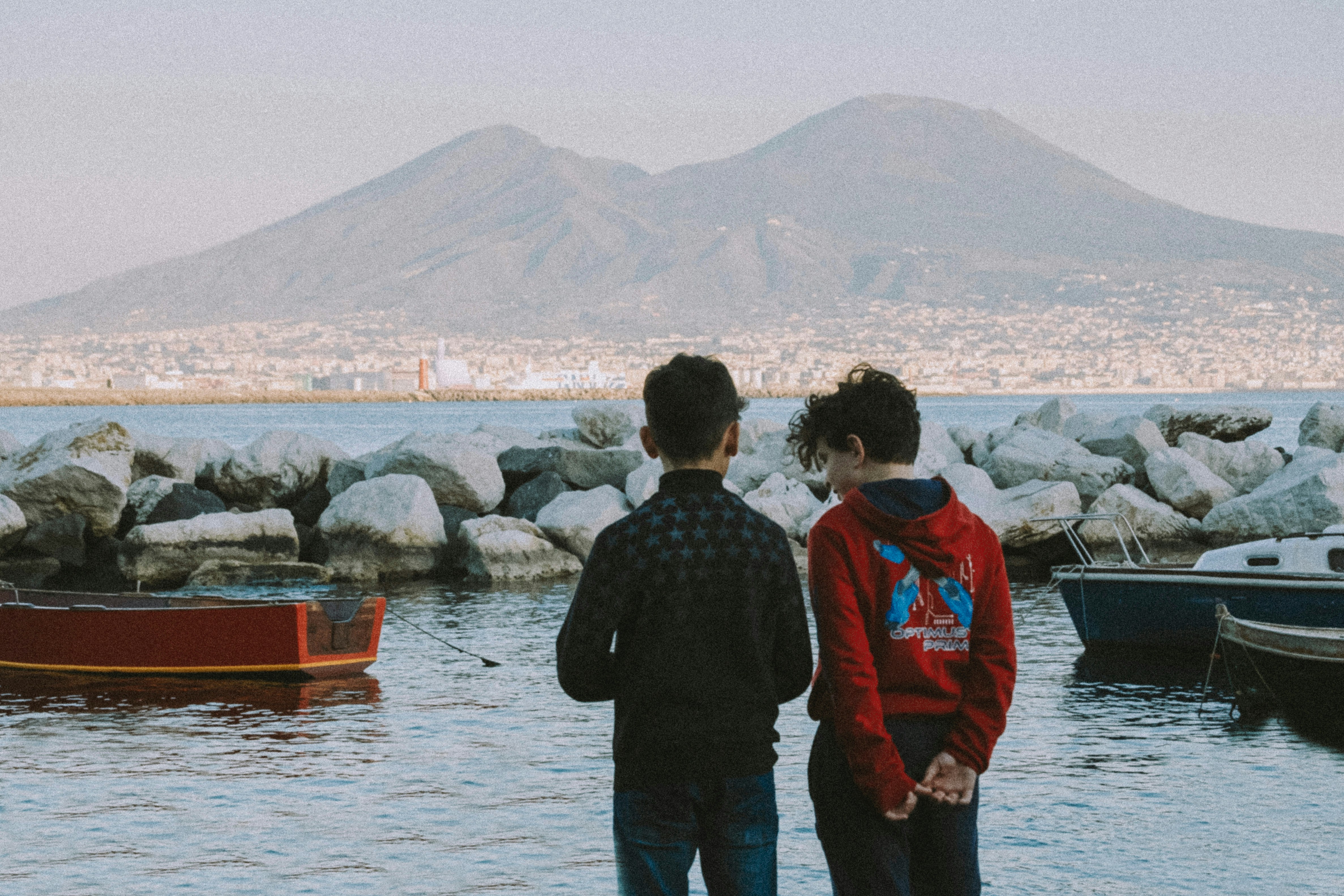 Harbor Reverie: Two Figures Watch Boats as Mountains Rise