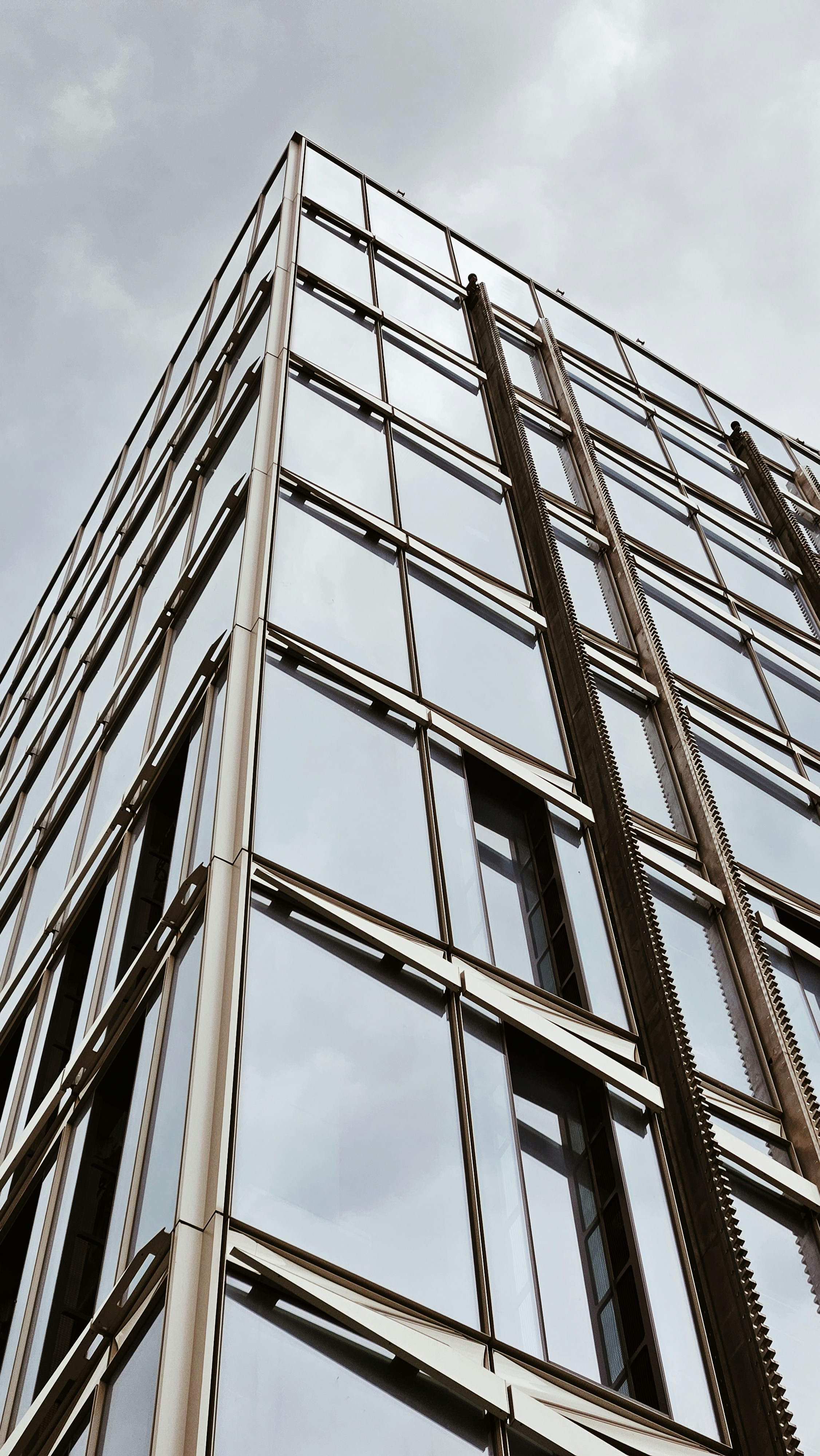 Angular glass building reflecting the overcast sky, showcasing contemporary architectural design.