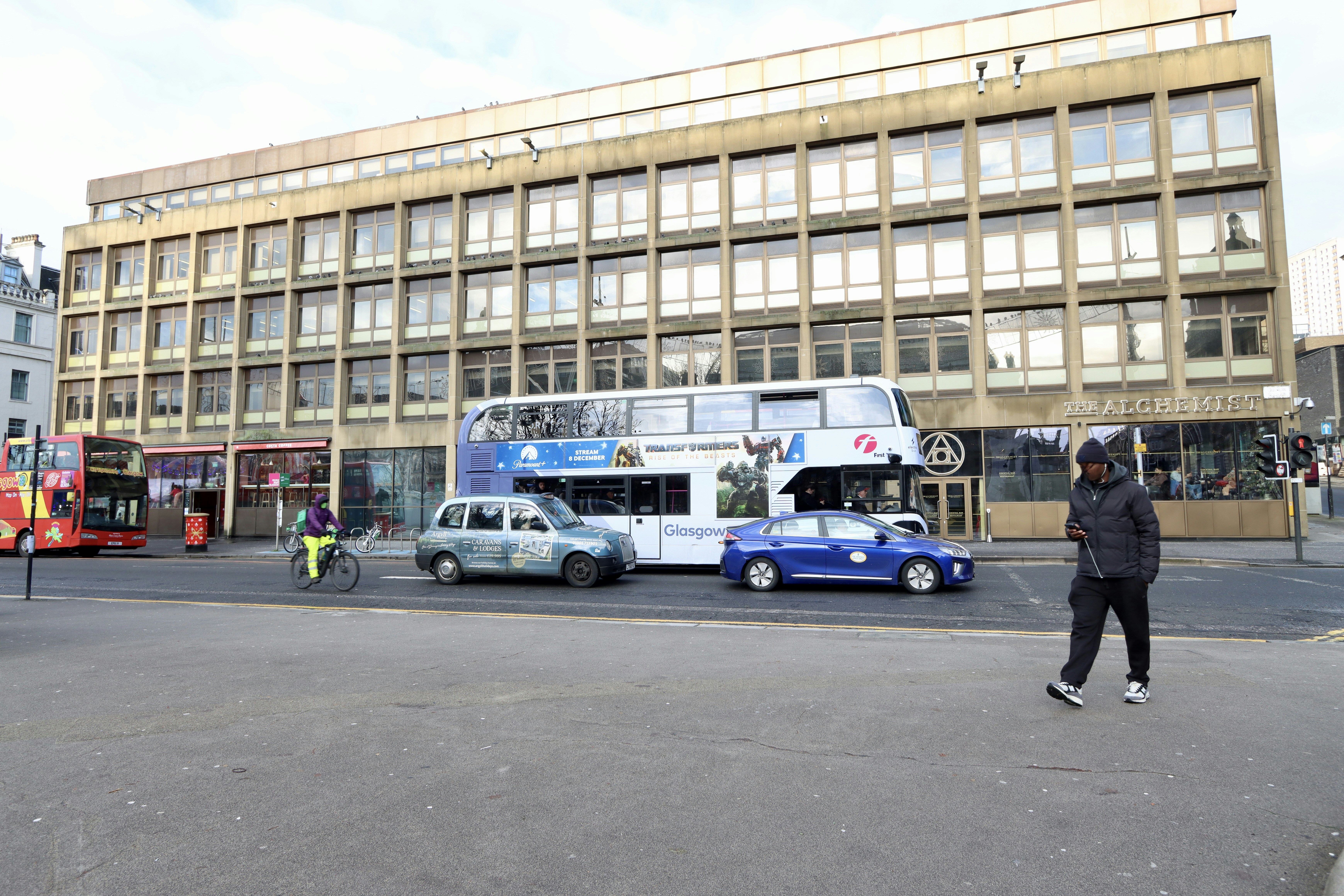 A busy urban street scene featuring a double-decker bus, parked cars, and pedestrians navigating the bustling environment.