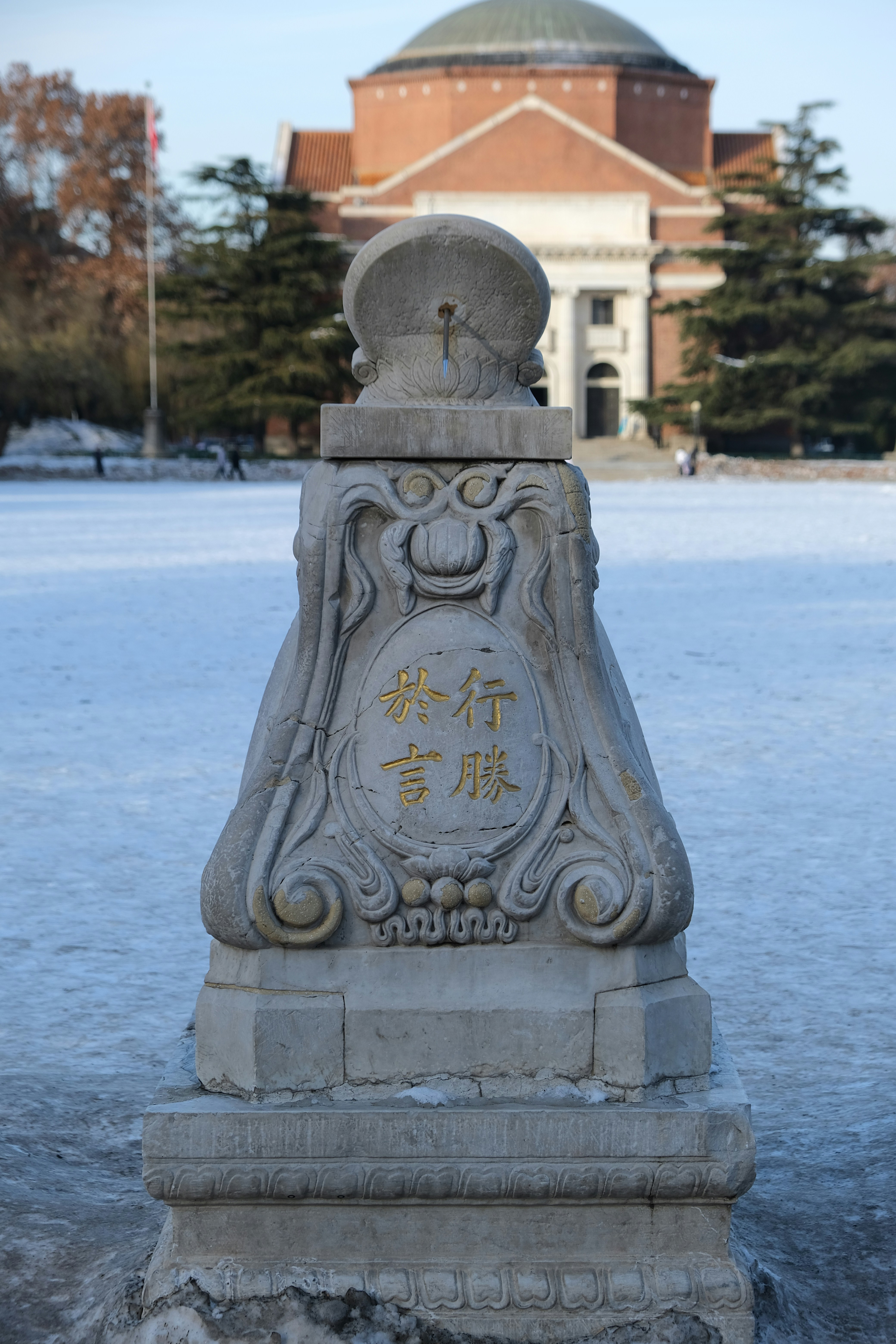 Golden Inscriptions on a Weathered Pedestal Framing a Snow-Covered University Dome