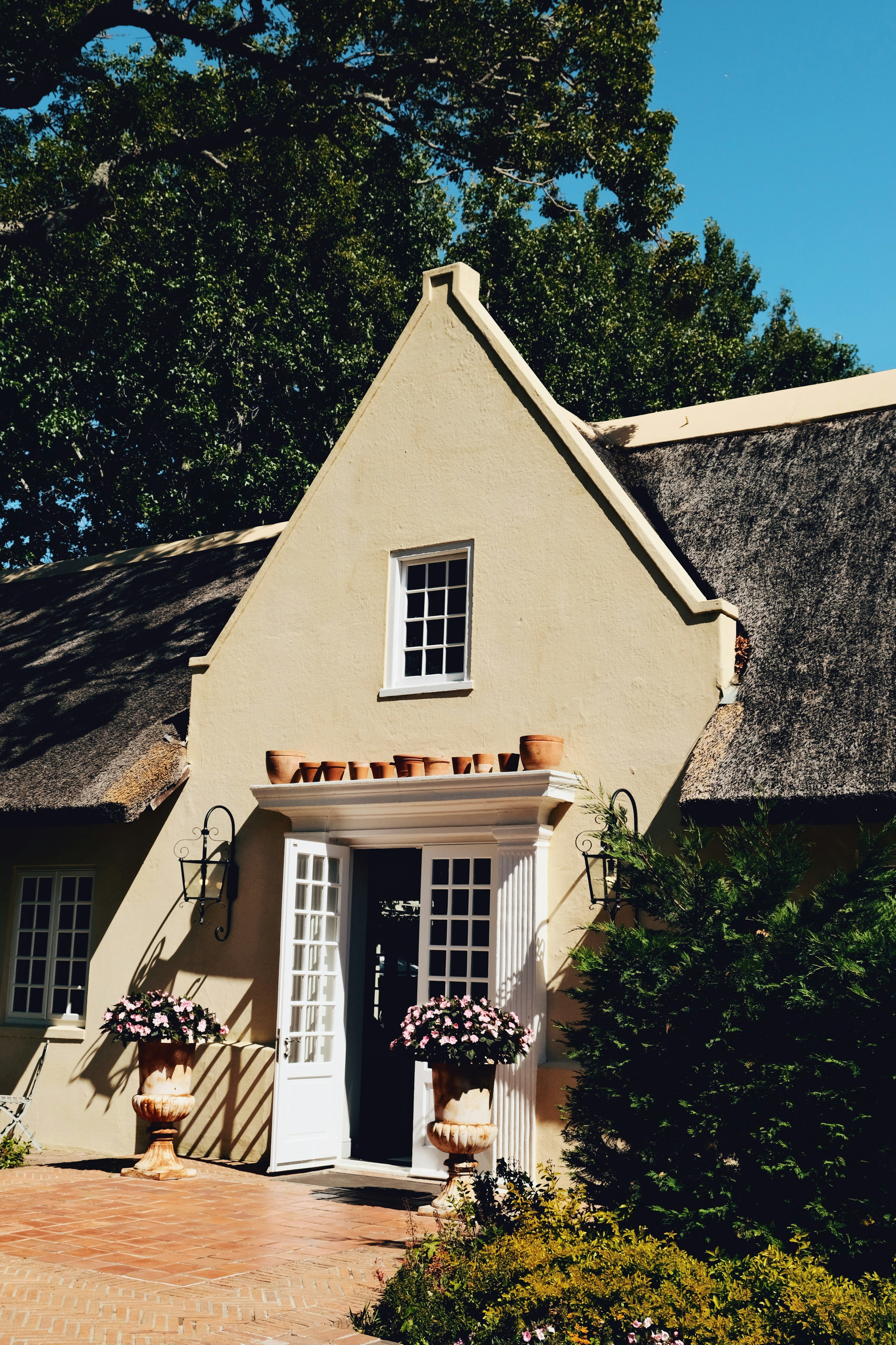 Pastel Cottage Entry: White Doors, Flower Pots, and a Thatched Roof