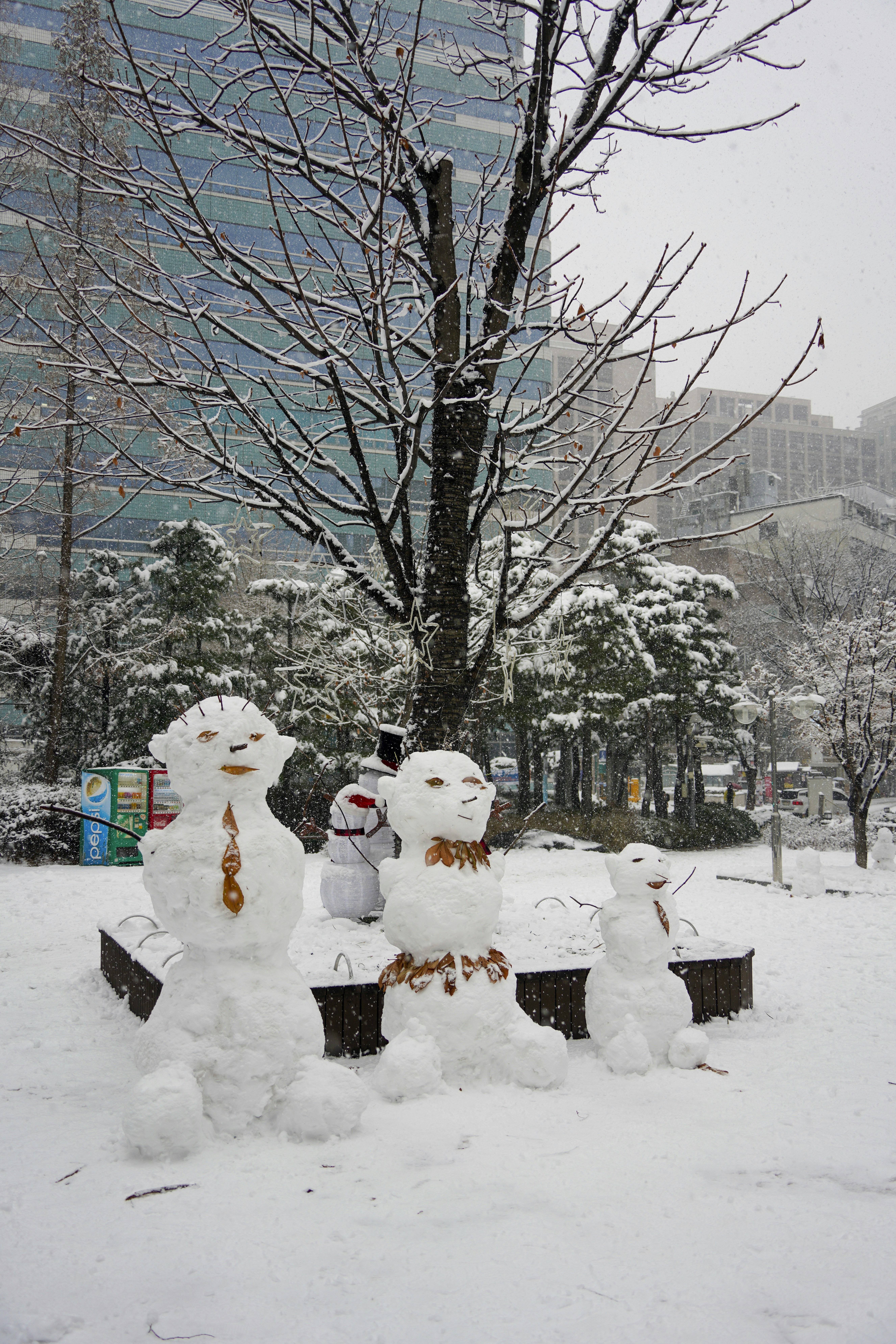 Three Snowmen Stand Watch Over a Quiet Snow-Covered City Park