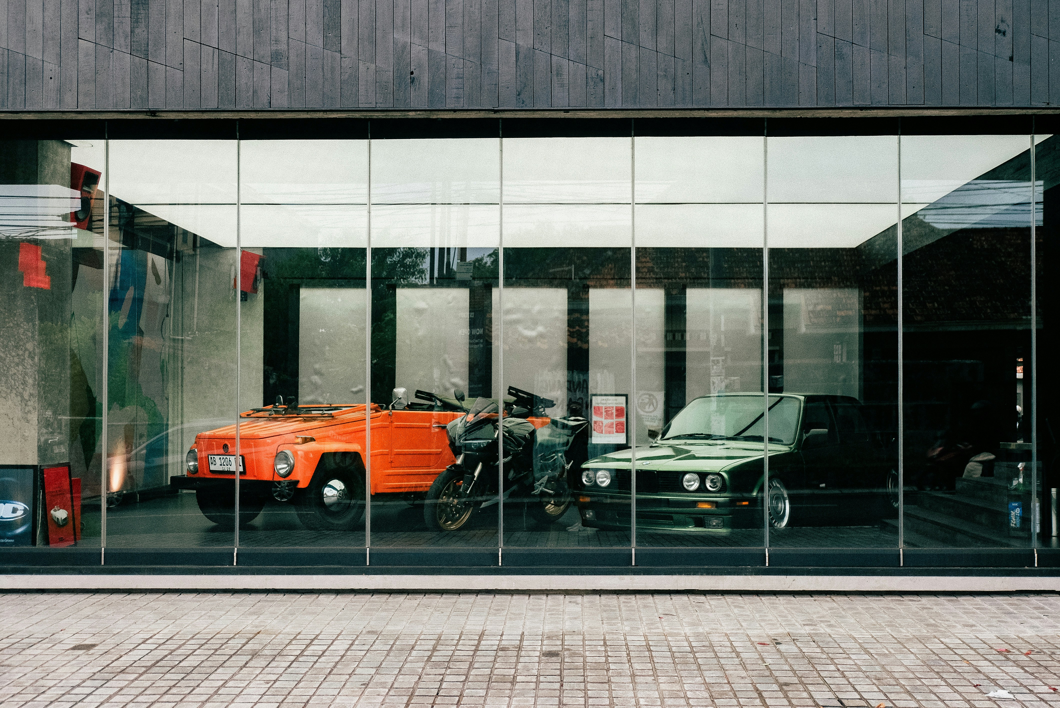 Glass-Front Showroom: An Orange Classic and a Motorcycle Framed by Reflections