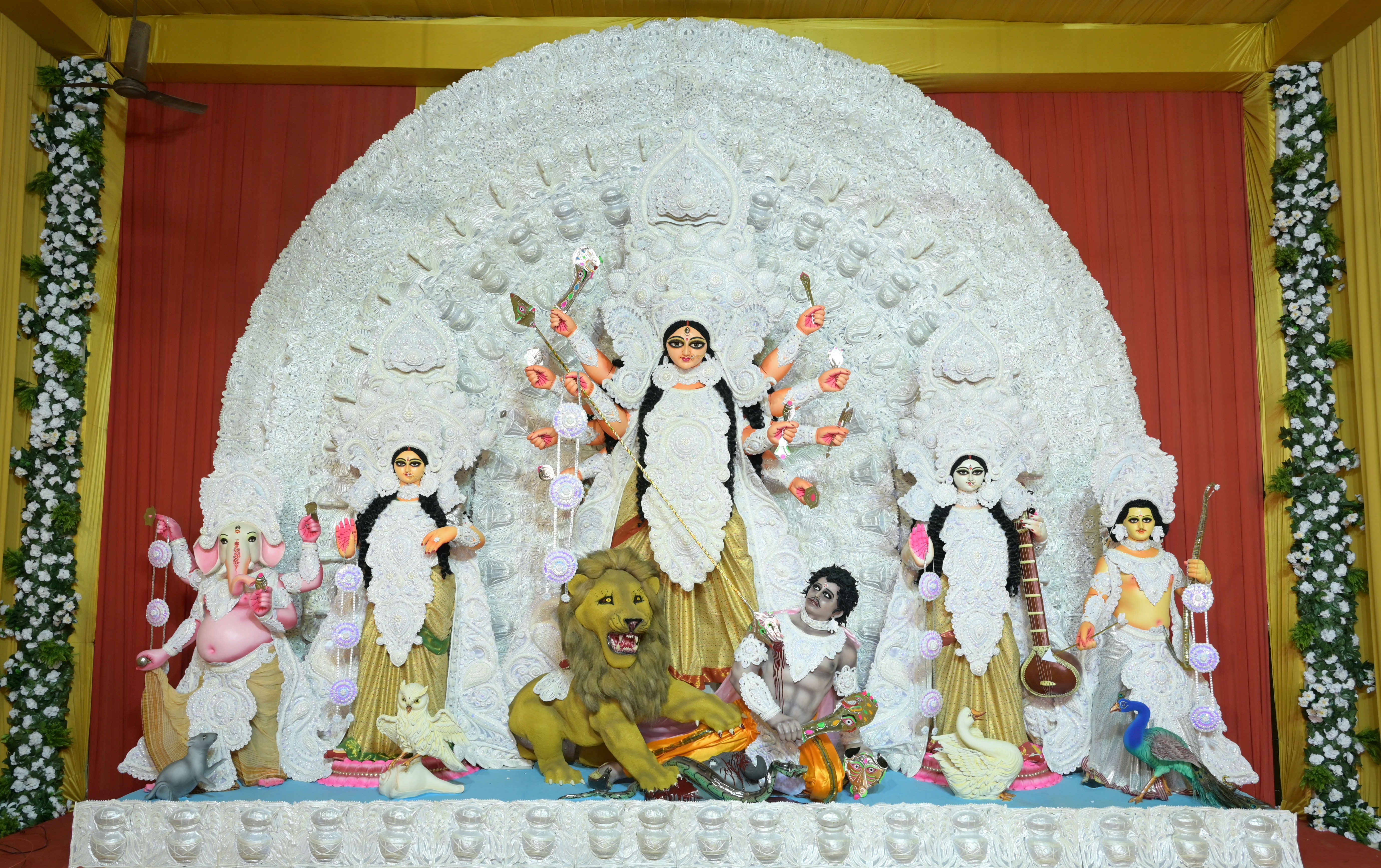 Elaborate Durga Puja idol arrangement featuring Durga, deities, and a lion against a decorative backdrop.