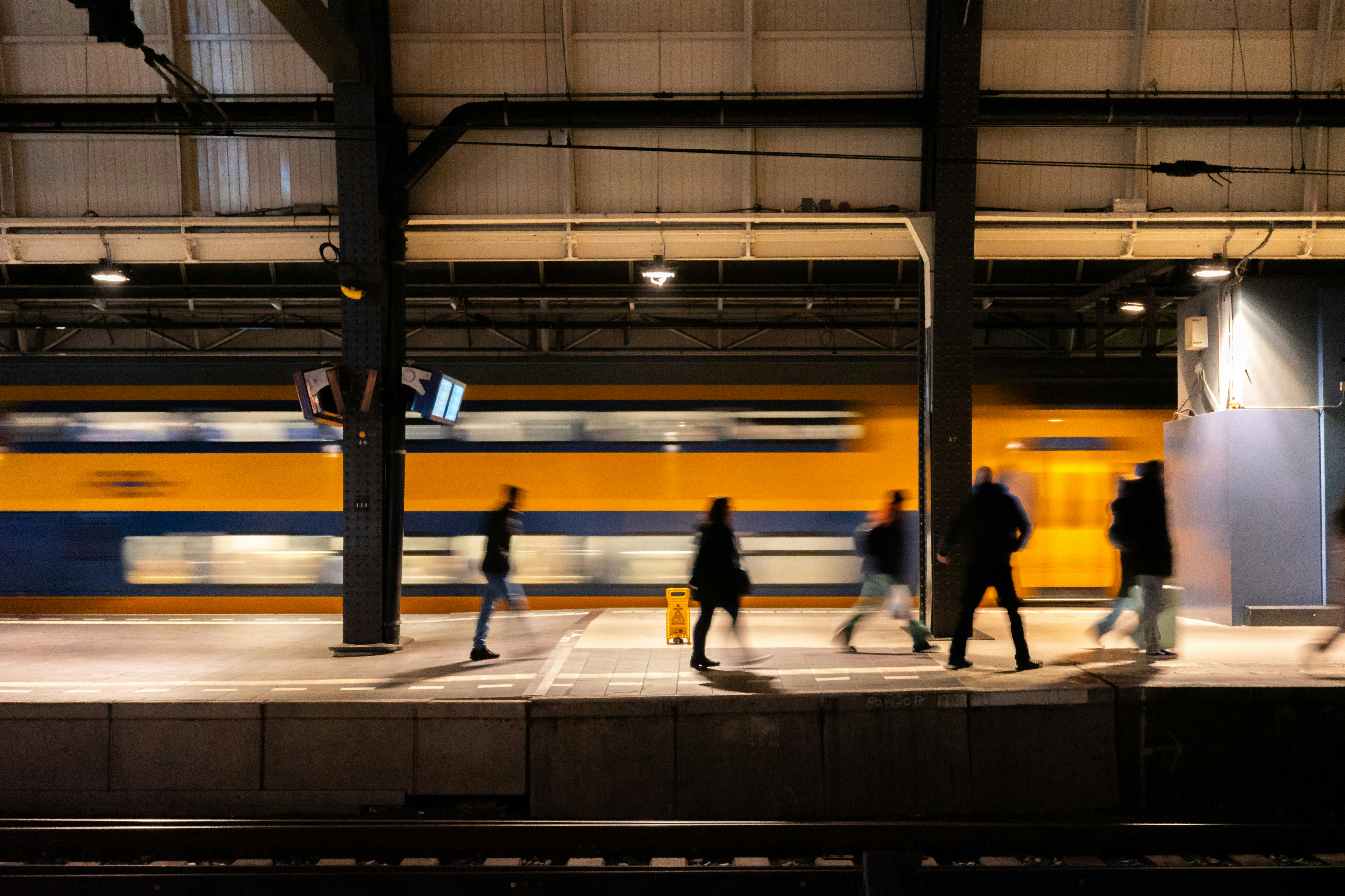 Silhouetted commuters moving swiftly along a platform as a train blurs past, capturing the essence of urban transit life.