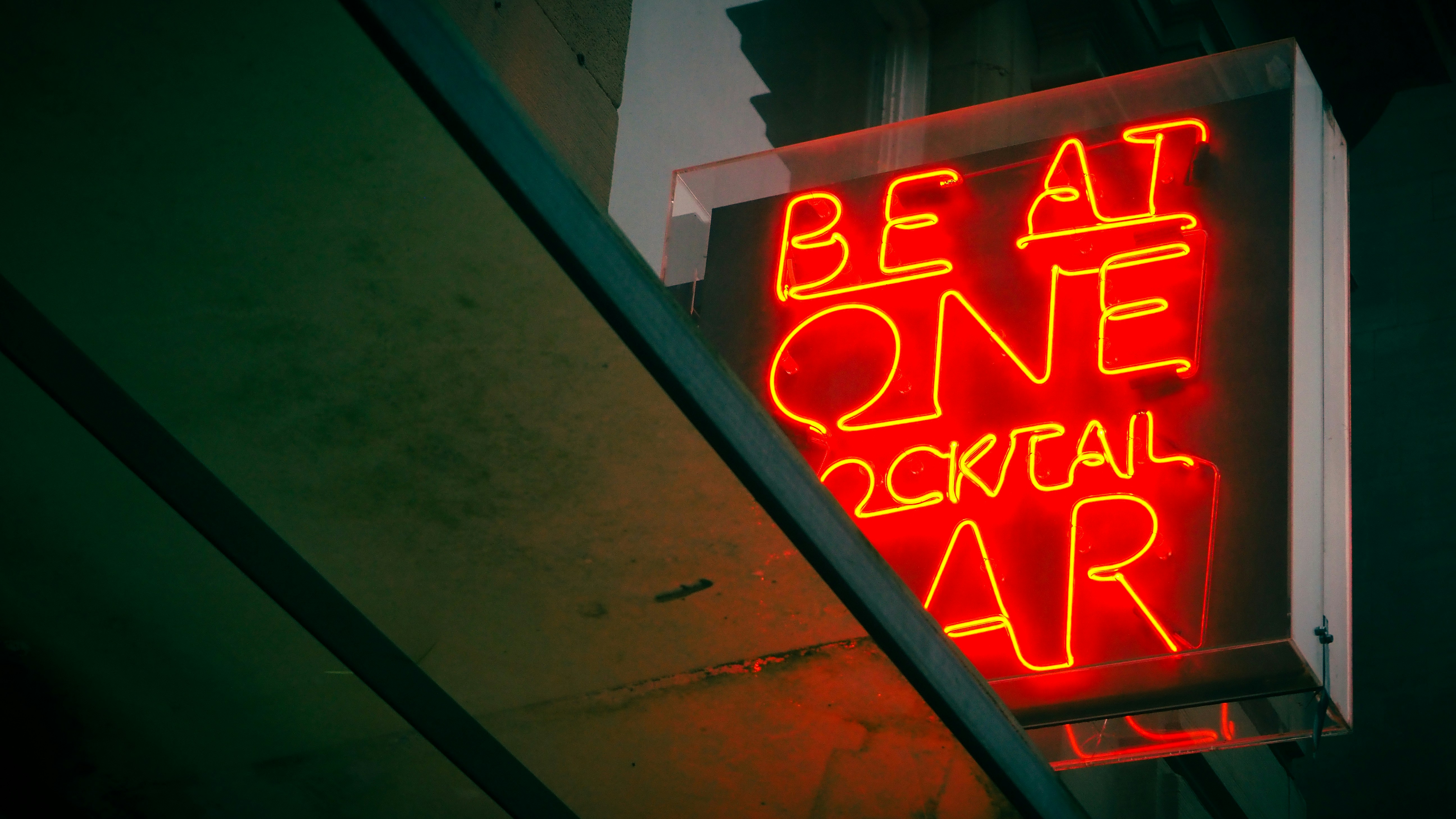 Neon sign for a cocktail bar glowing against a dim urban backdrop.