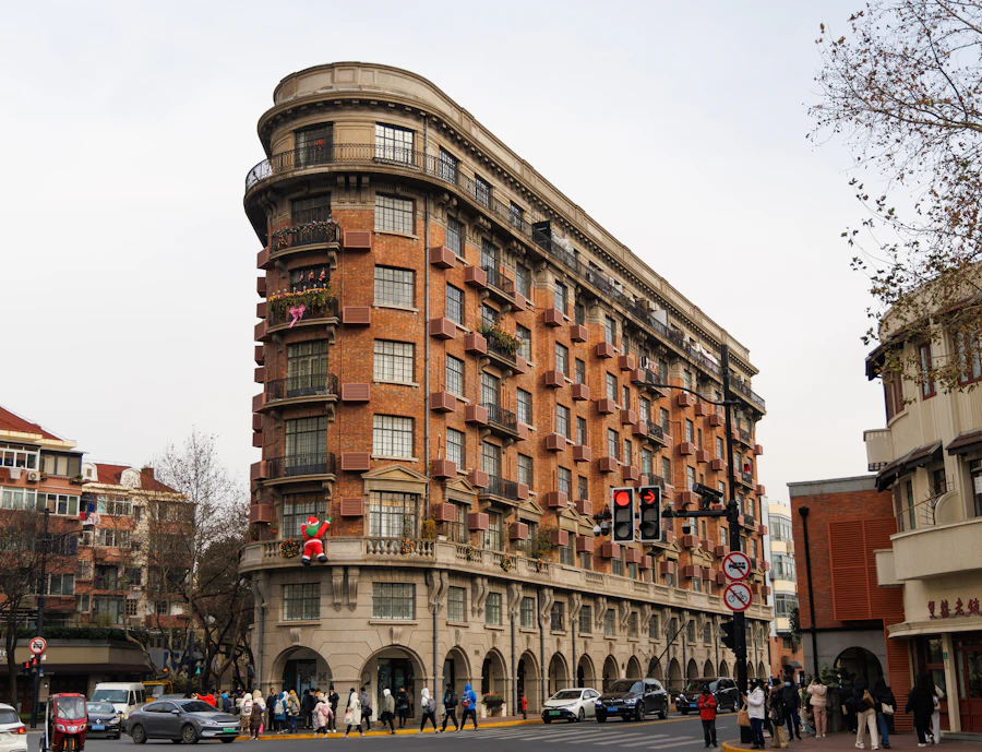 A curved brick apartment building anchors a busy urban intersection, with pedestrians, cars, and traffic lights below. Bare winter trees and overcast sky frame the scene.