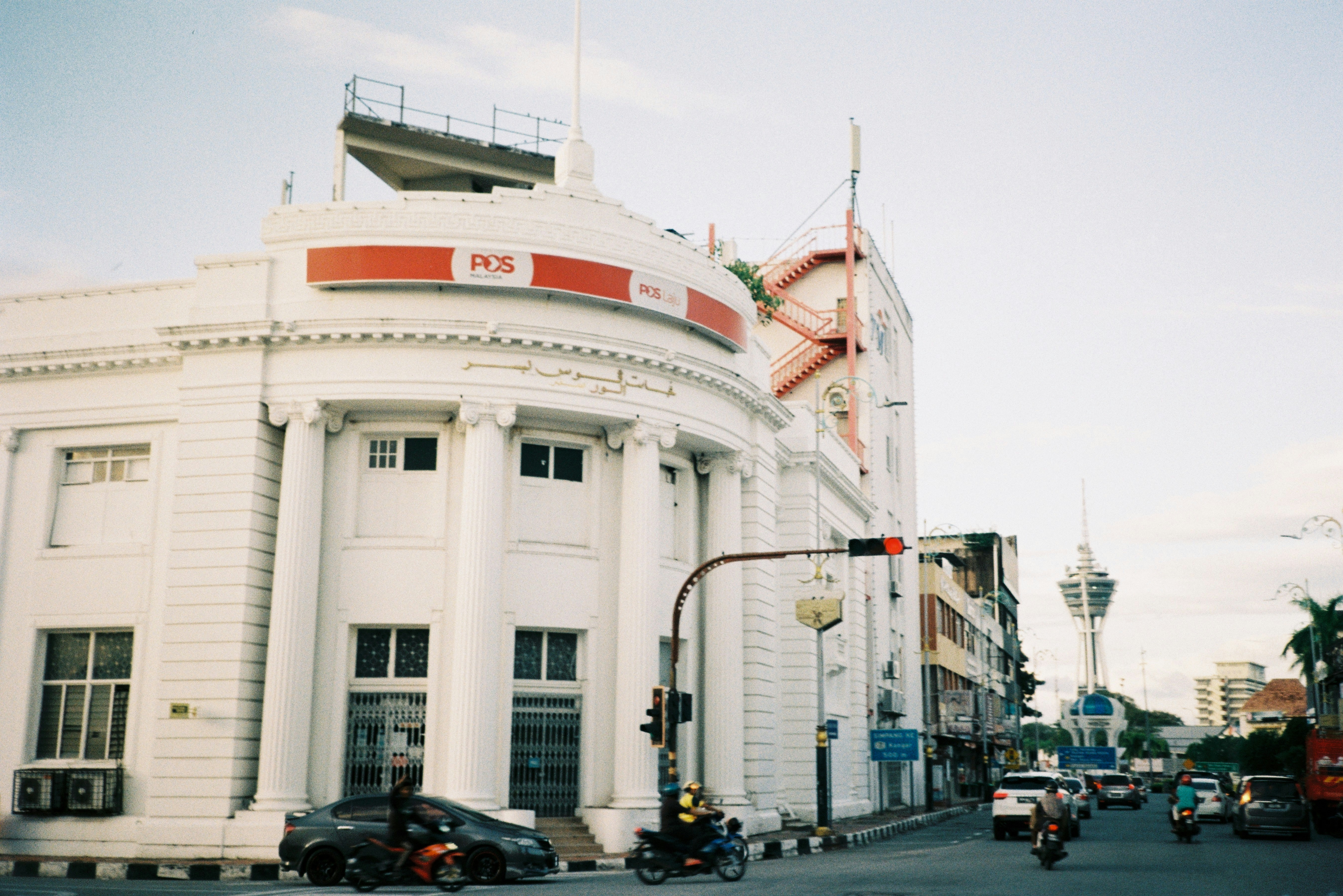 White colonial-style building with columns and red accents on a busy street corner under a clear sky.